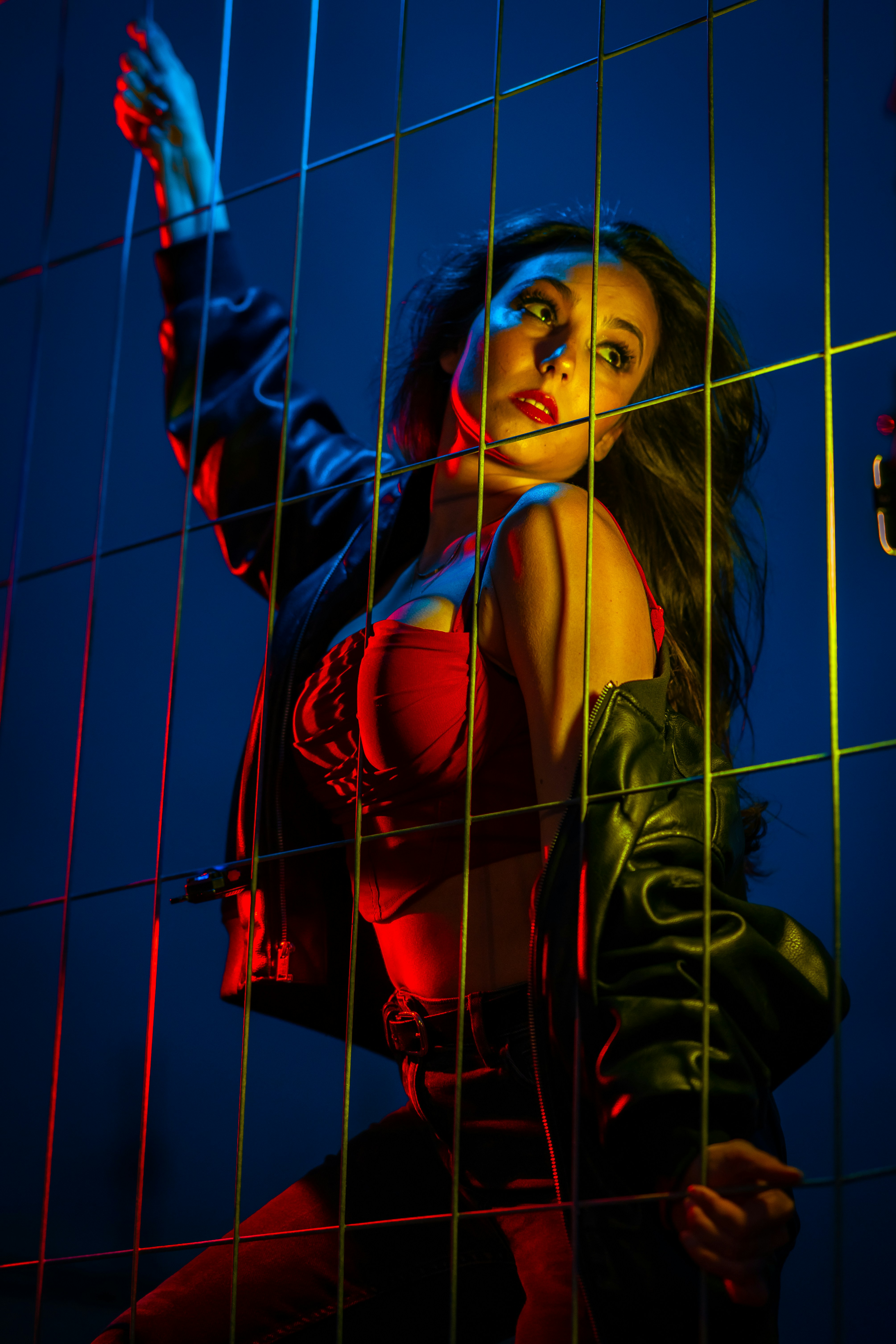 A woman in a black leather jacket behind a metal grid in neon light