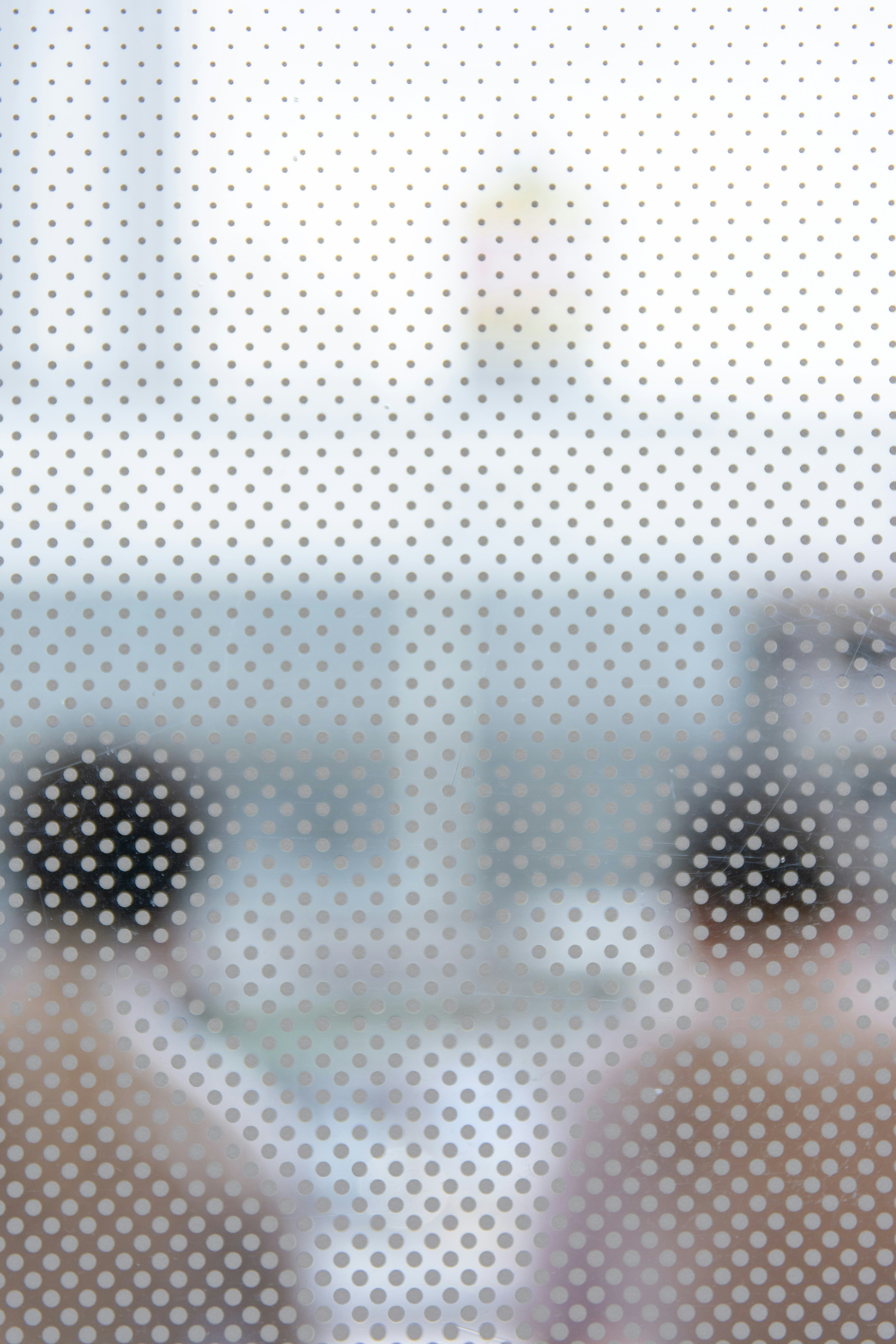 Hazy office environment visible through frosted glass with dotted pattern; foreground obscures details, leaving silhouettes of furniture and a person out of focus. This is a decorative/abstract shot.
