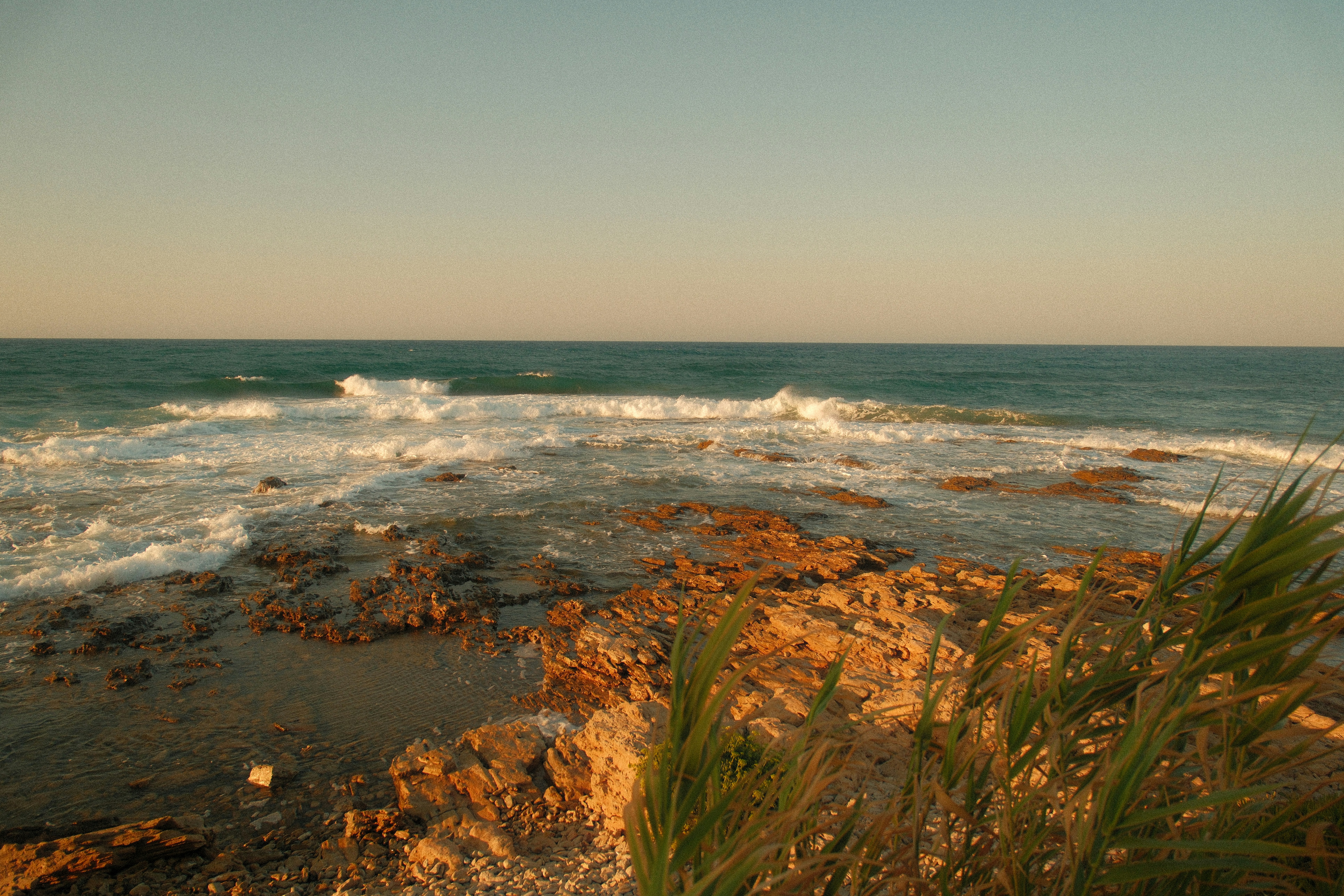 Sunlit Shoreline: Rocks, Sea Spray, and Coastal Grass