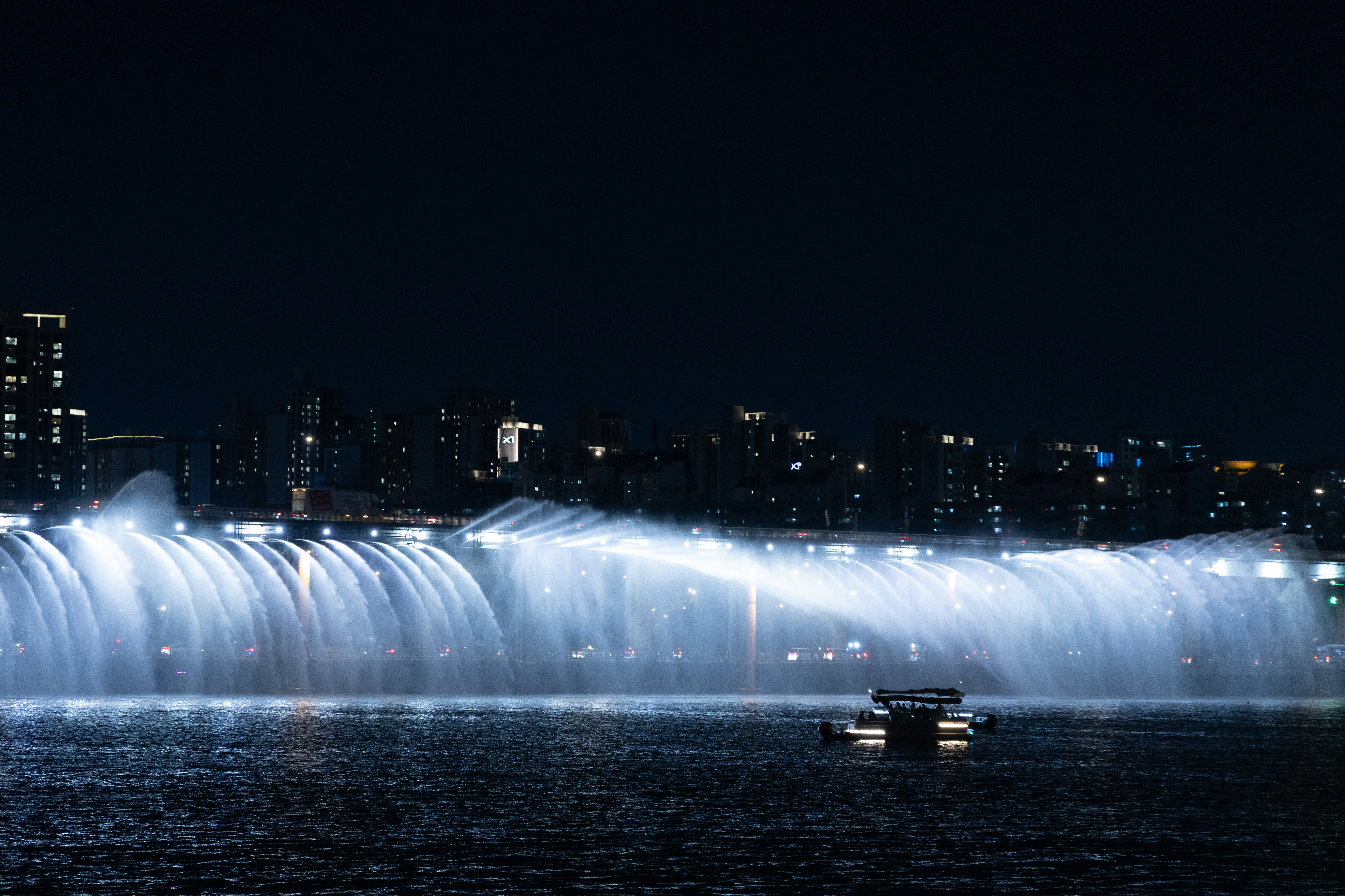 Moonlit Waterfront: Nightscape of a Water Curtain Over a Quiet City