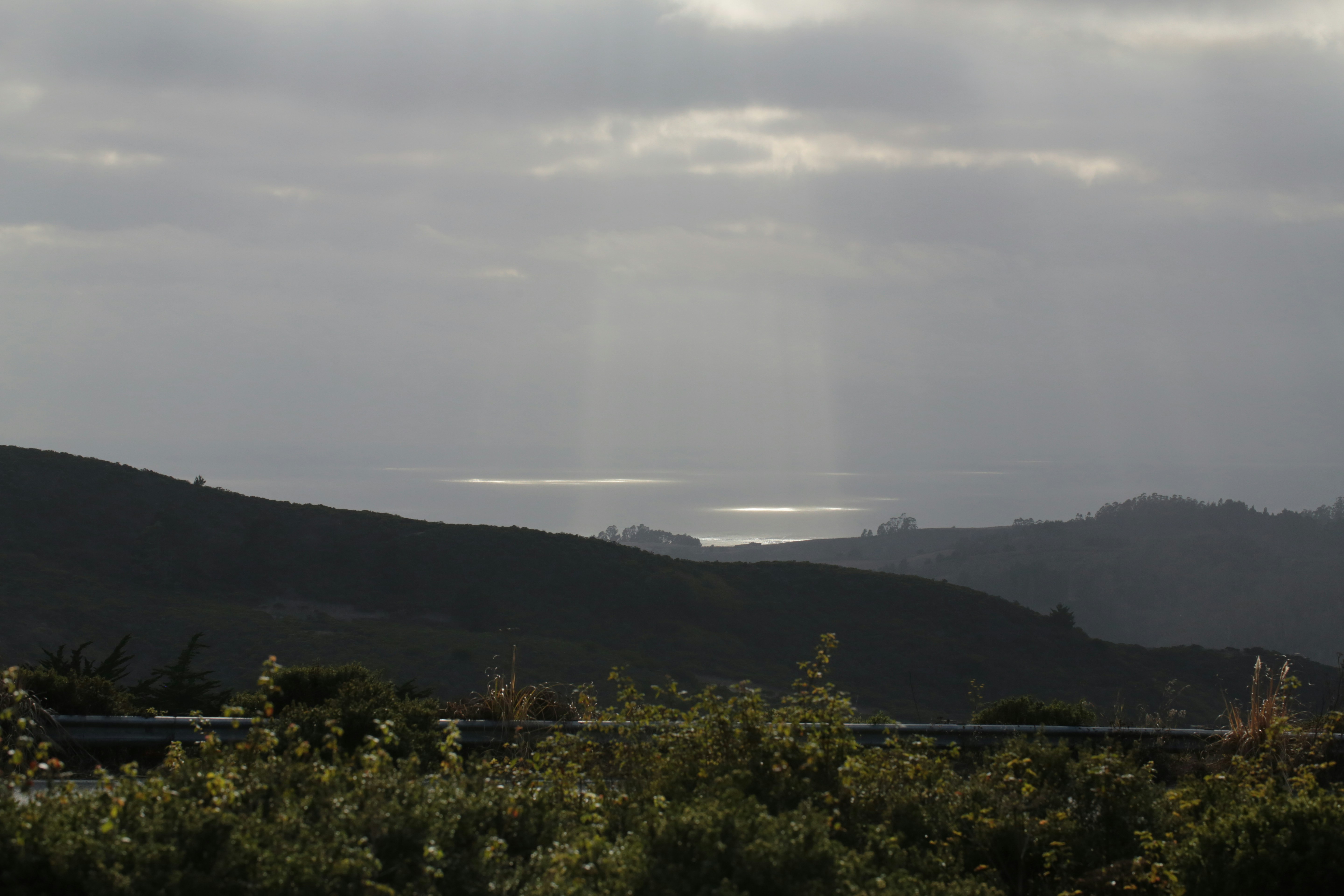 Sunbeams over distant coastline through a calm hillside