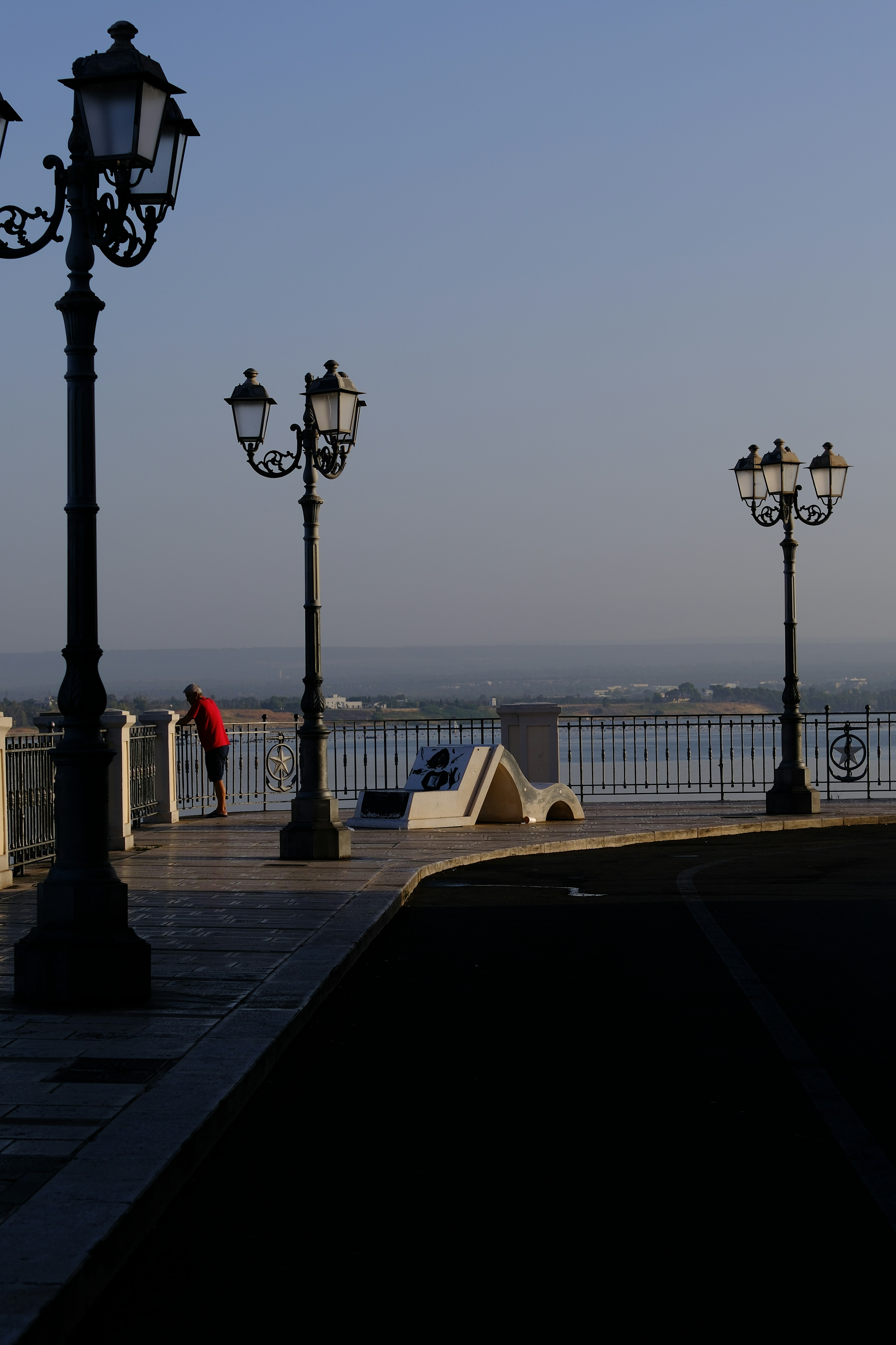 Red-robed onlooker at a coastal promenade under ornate lampposts