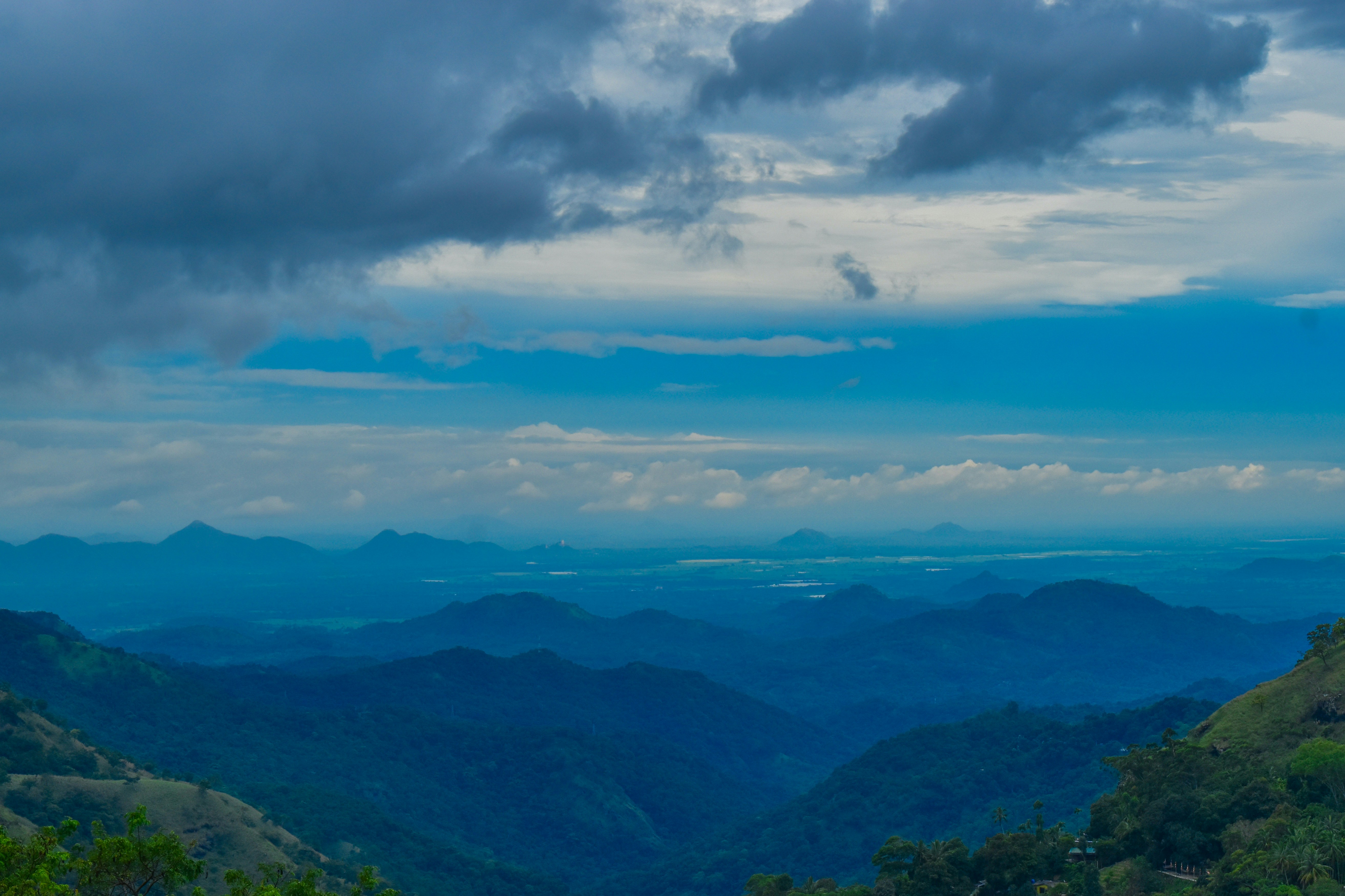 Serene mountain panorama with layered ridges fading into a distant haze under a partly cloudy sky. A vast valley stretches across the frame, emphasizing depth and distance.