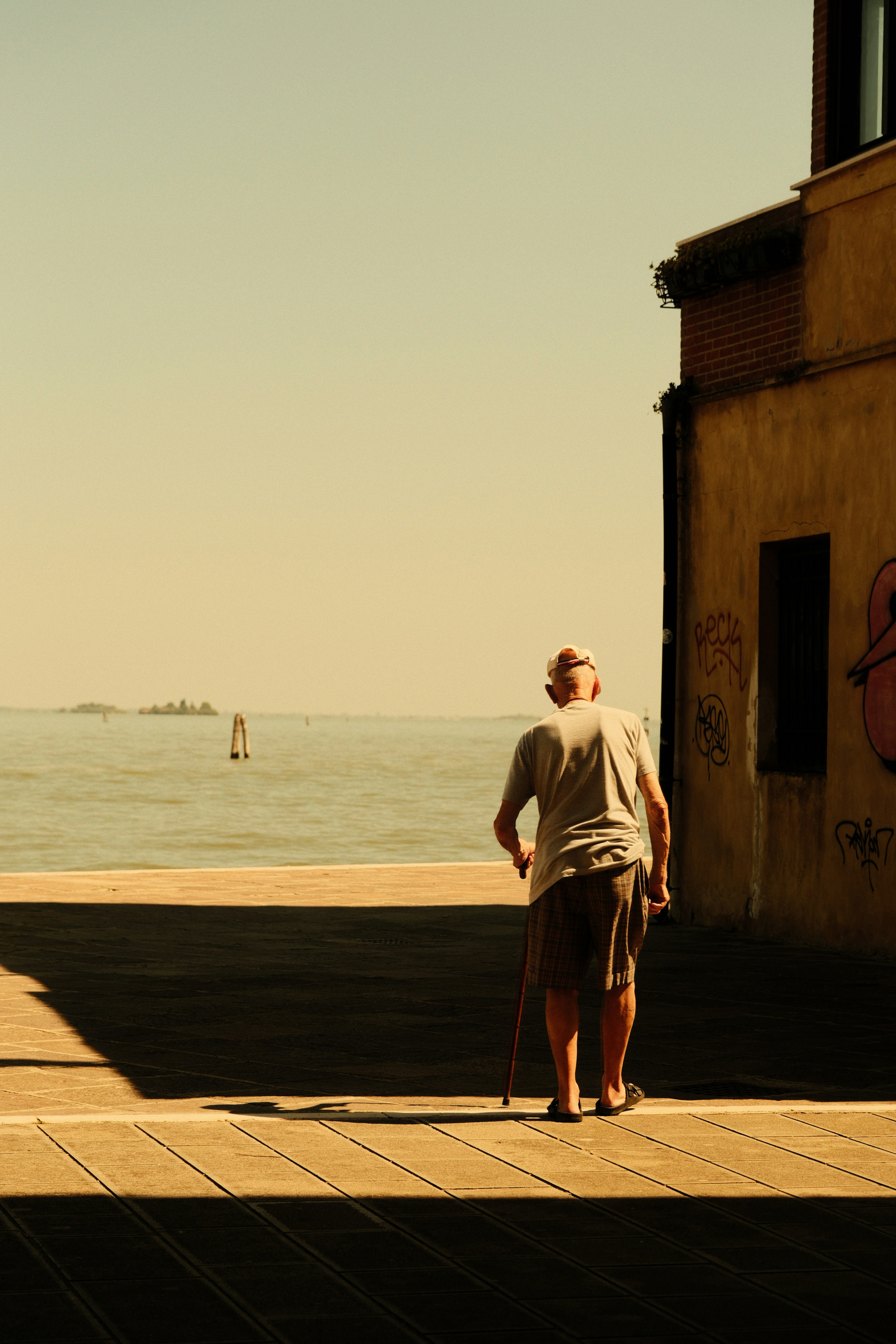 Sunlit Seaside Stroll: An Elderly Figure by the Graffiti walls