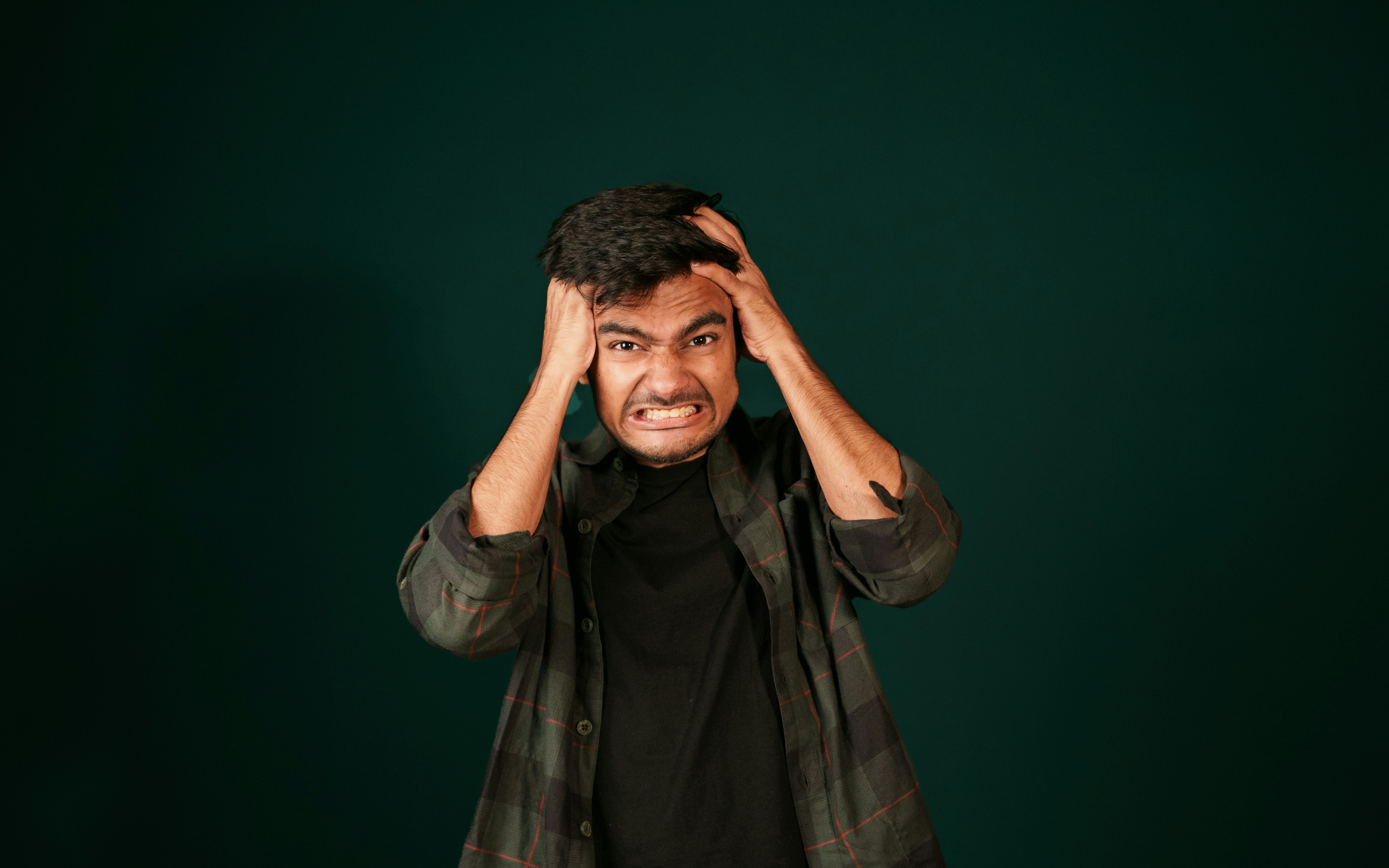 Frantic Grip: A Man Clutches His Head Against a Dark Green Backdrop