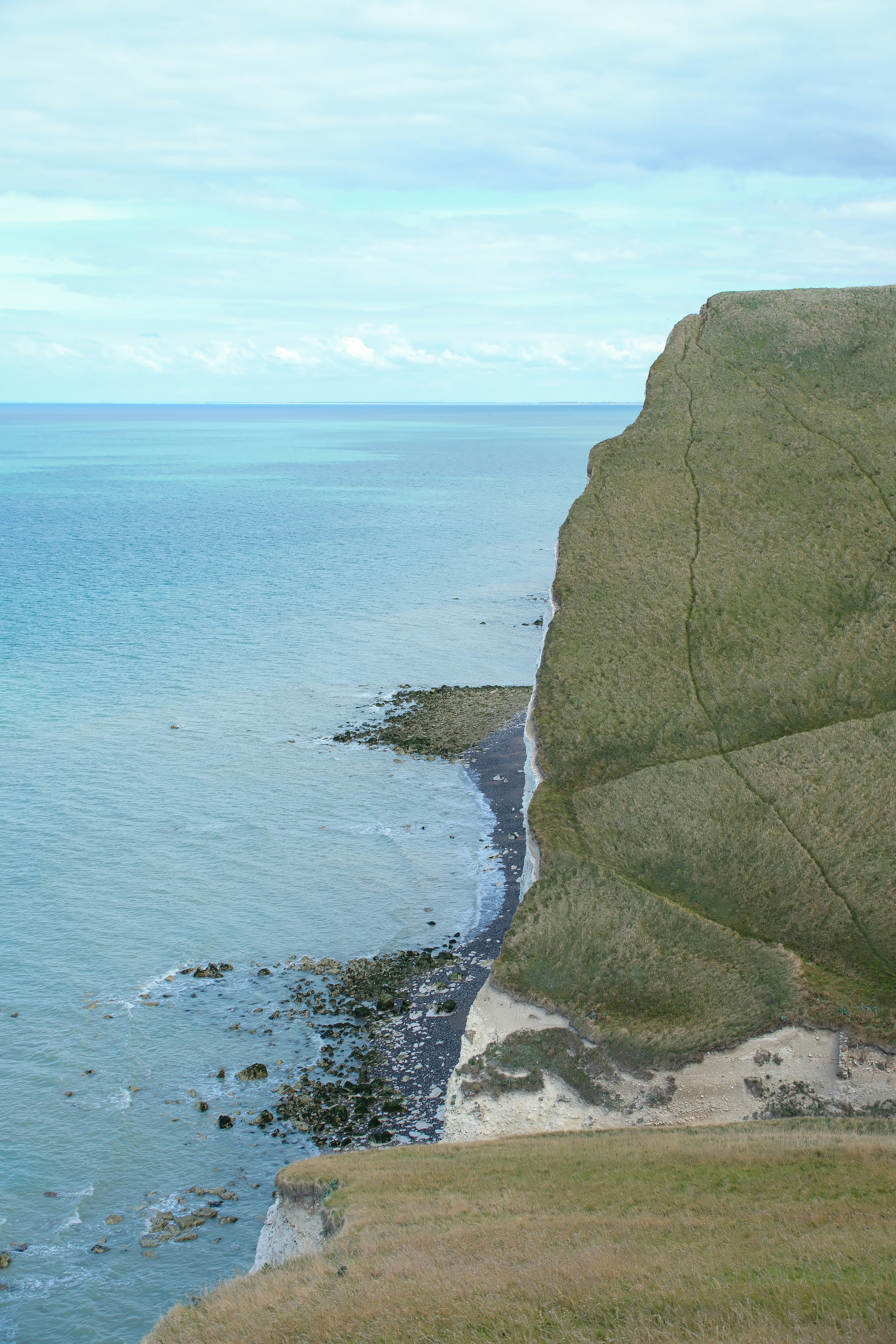 A quiet, minimalist view of the Alabaster Coast, where soft grassy slopes fall toward a calm blue‑green sea.