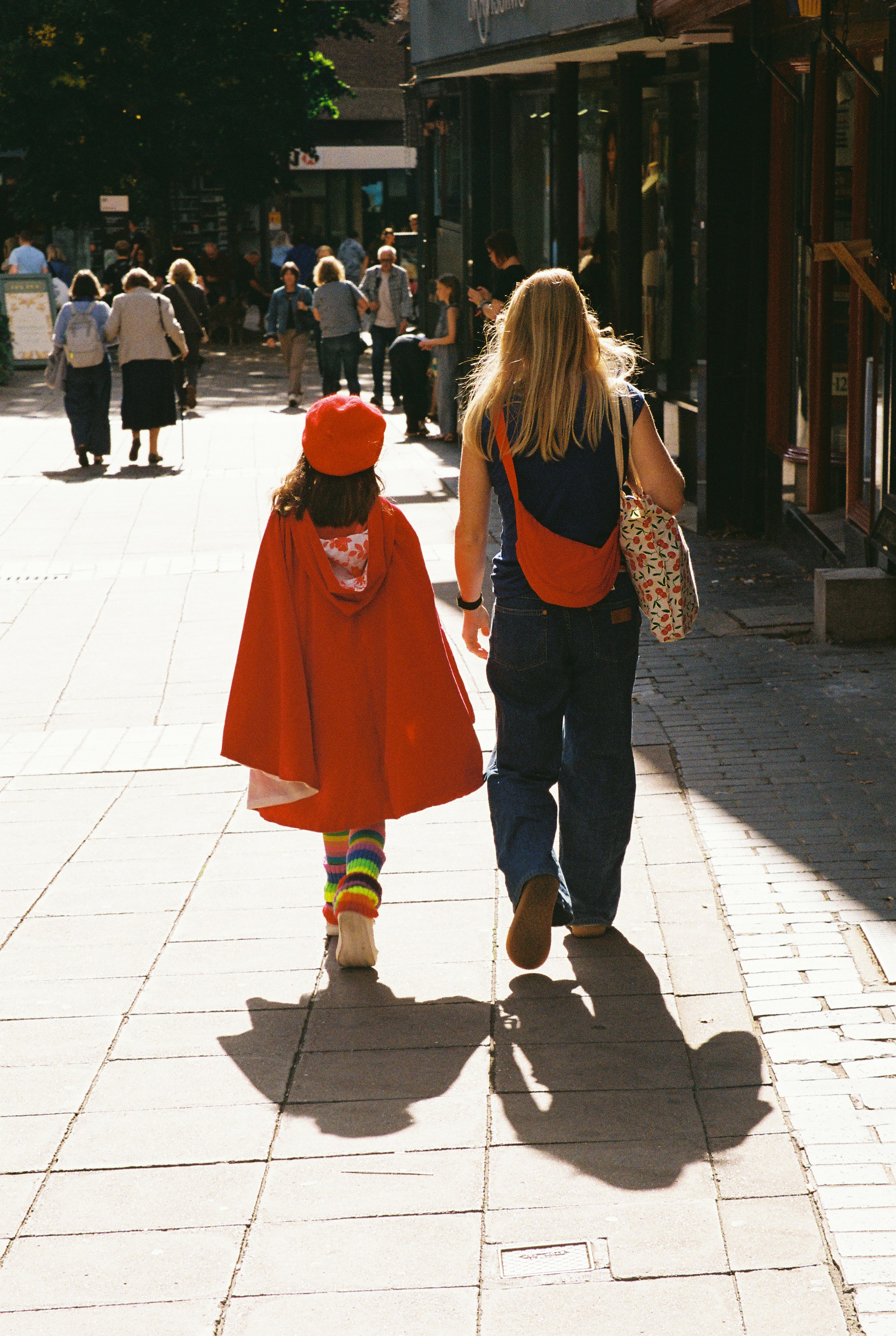 Two Walkers, One Street: A sunlit stroll with a splash of red