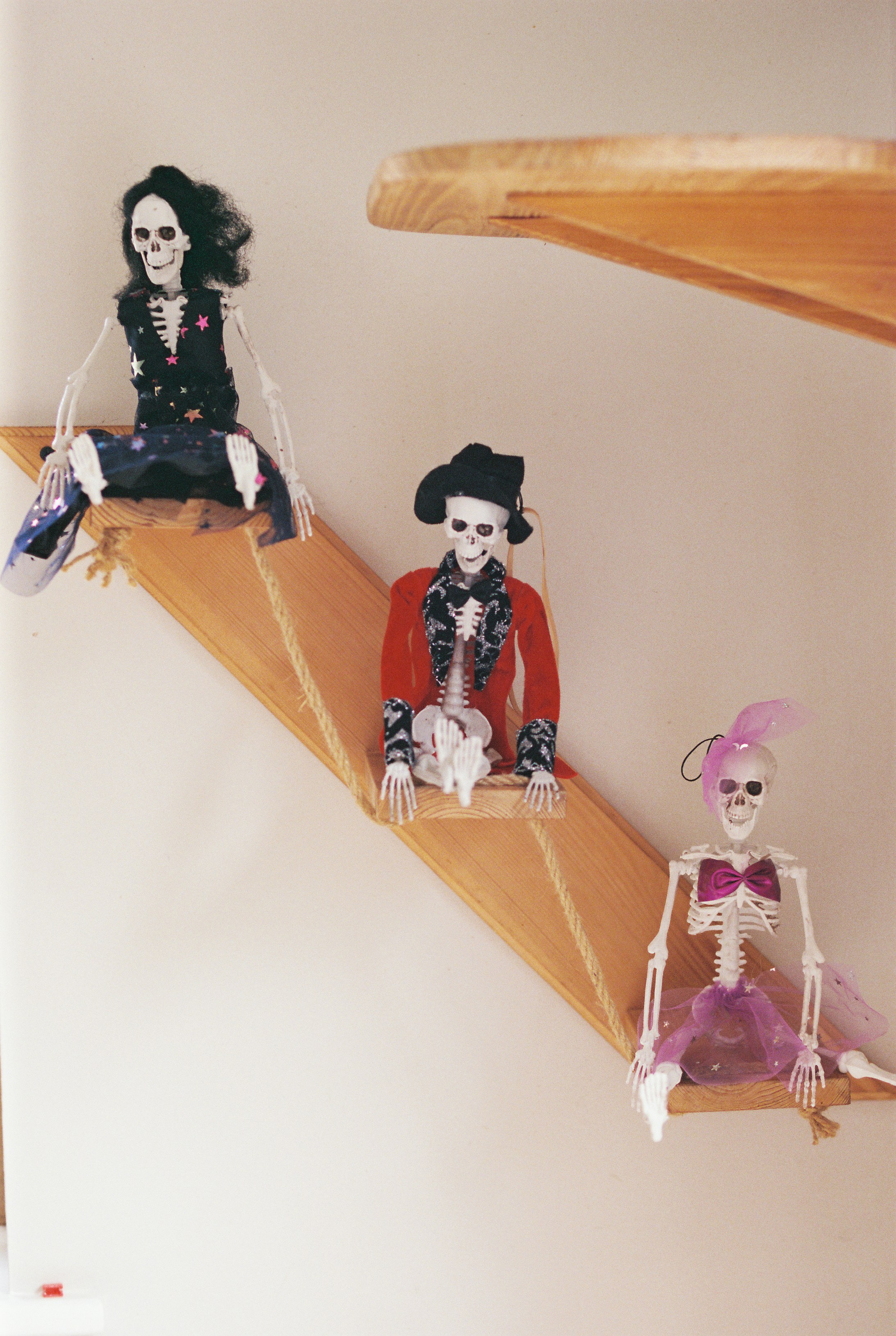 Three skeletal figurines dressed in colorful outfits perch along a wooden staircase, creating a playful Halloween display.