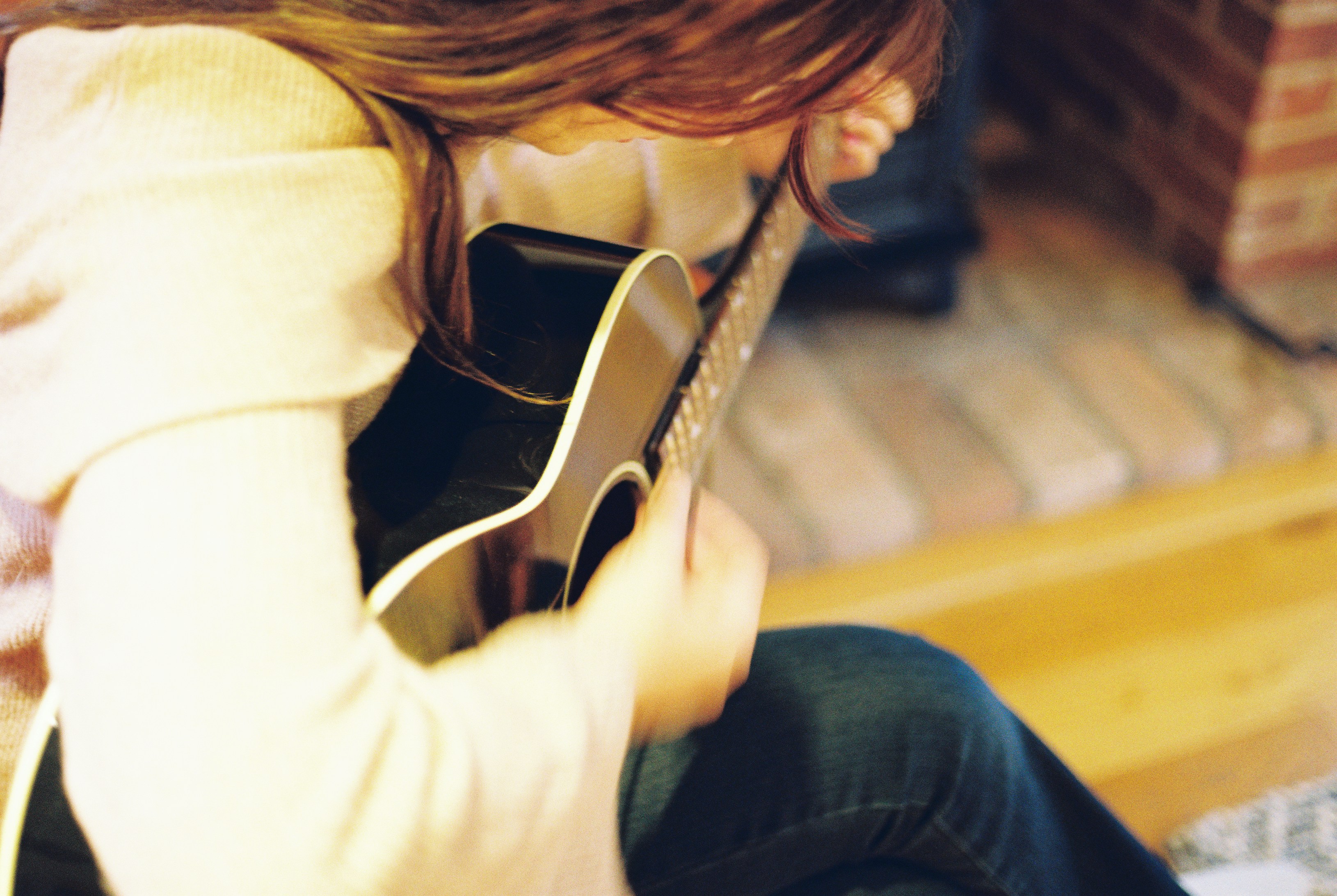 A soft-focus, intimate view of a person playing an acoustic guitar, seated on a wooden step; the image emphasizes the instrument and the gentle movement of the hands. This is a candid photograph rather than a painting or illustration.