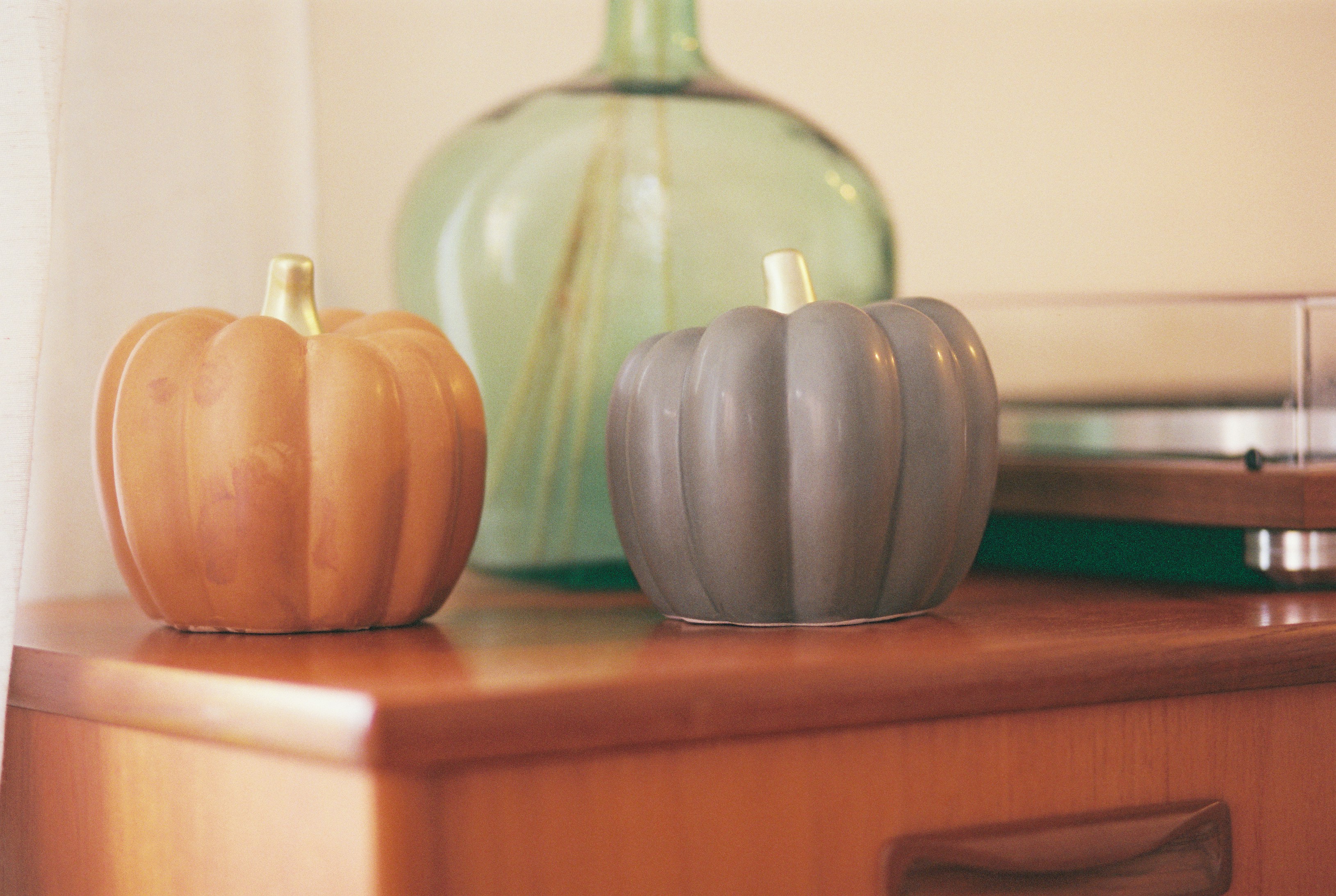 Two Ceramic Pumpkins on a Wooden Dresser with Glass Vase in the Background