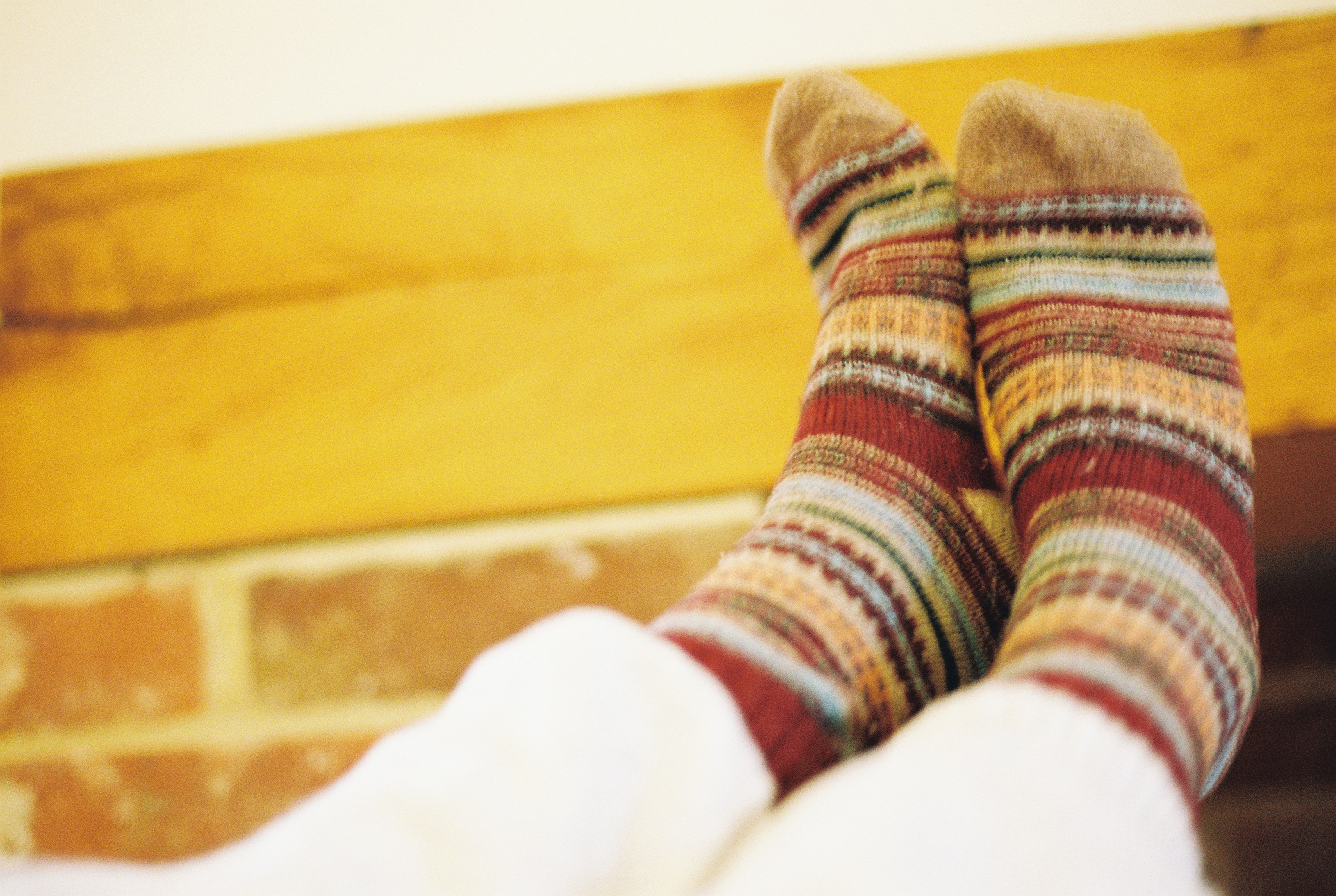 Colorful striped socks rest against a warm brick-and-wood backdrop, inviting a relaxed, cozy mood.