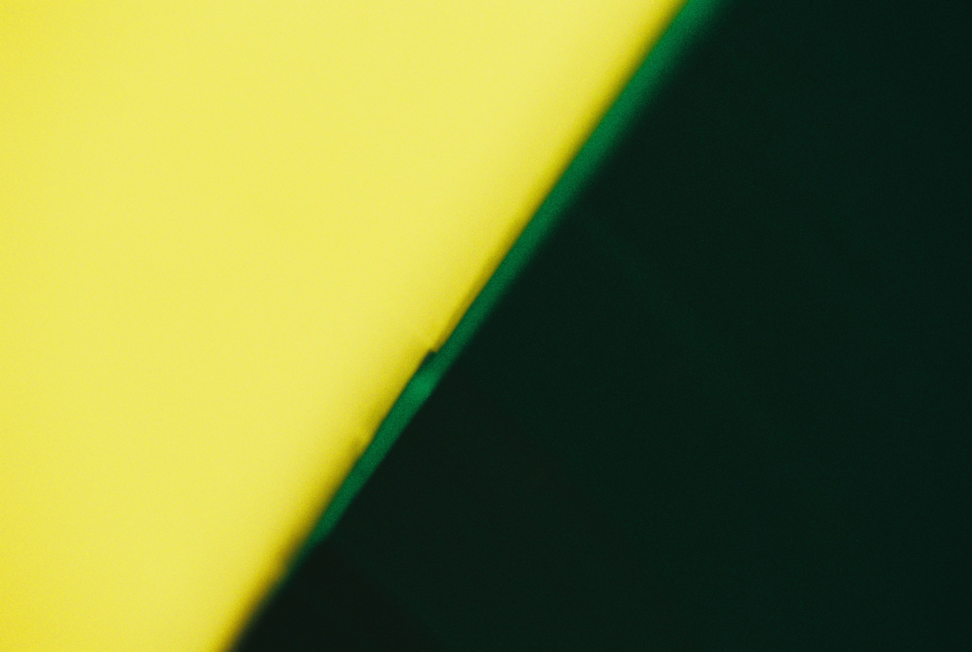 Diagonal composition with a vivid yellow field meeting a dark emerald edge along a sharp crease; abstract close-up emphasizing color contrast and texture. This is a photographic study of color-block geometry.