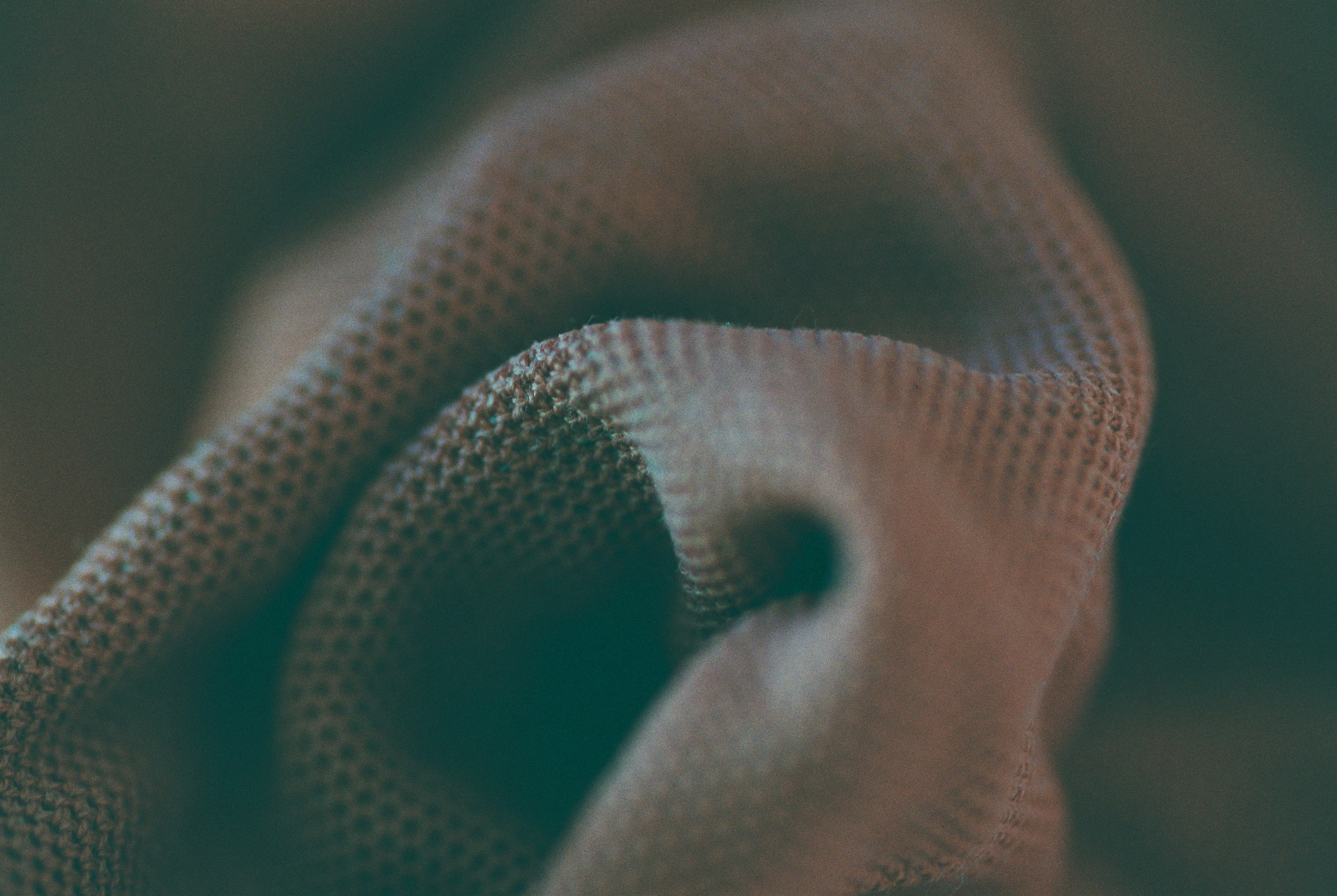 Close-up of a softly folded, perforated fabric with a teal-green hue and shallow depth of field, highlighting fine mesh texture and subtle light play.