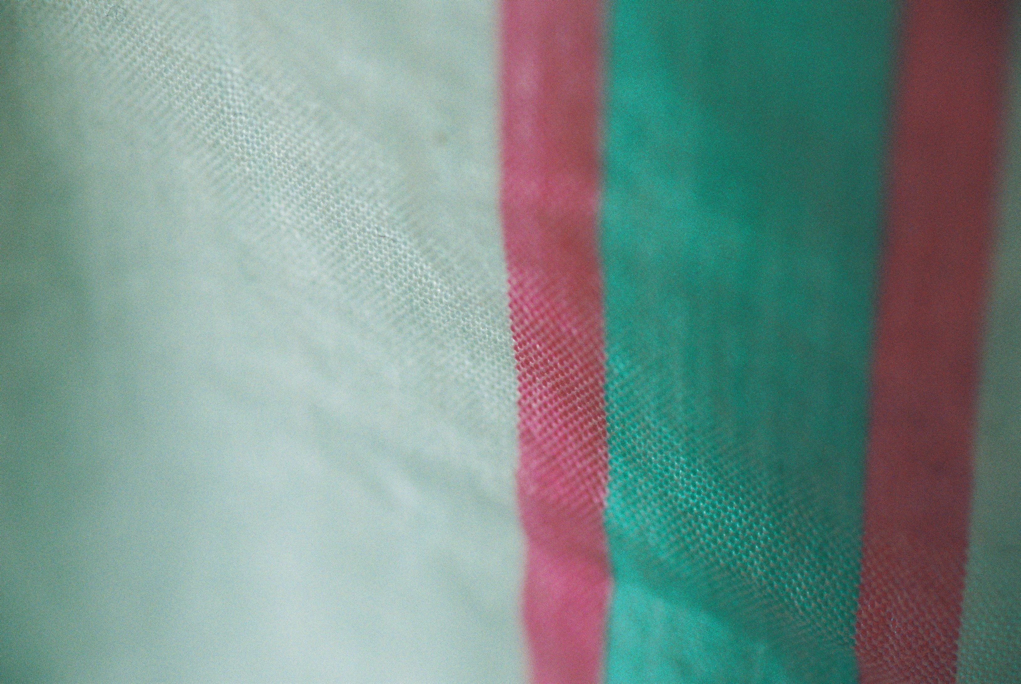 Close-up of striped fabric with teal and magenta bands and soft weave texture, emphasizing color and thread detail in a macro view.