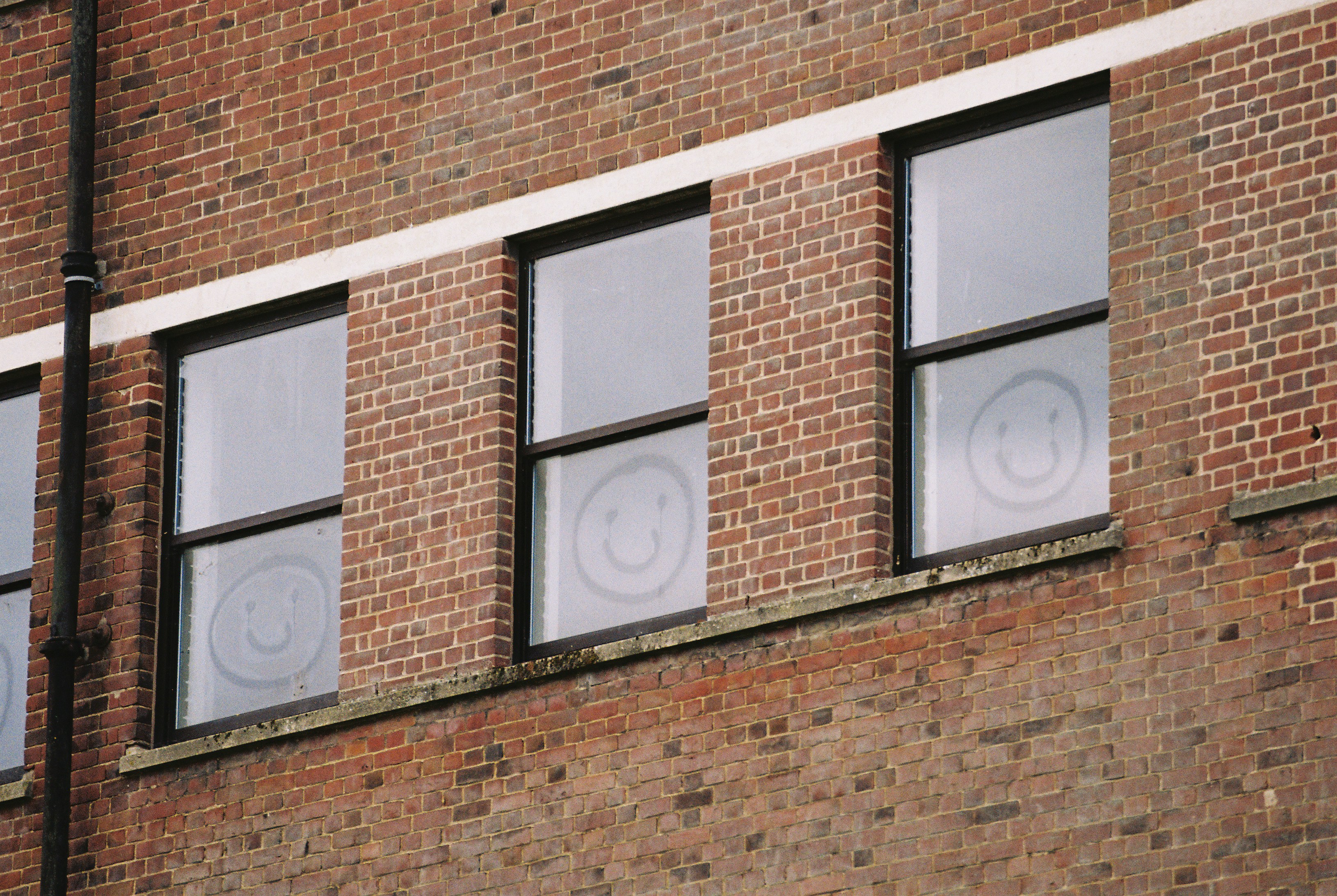 Brick building with three rectangular windows; faint circular window decals visible through the glass, suggesting an interior display or privacy screens.