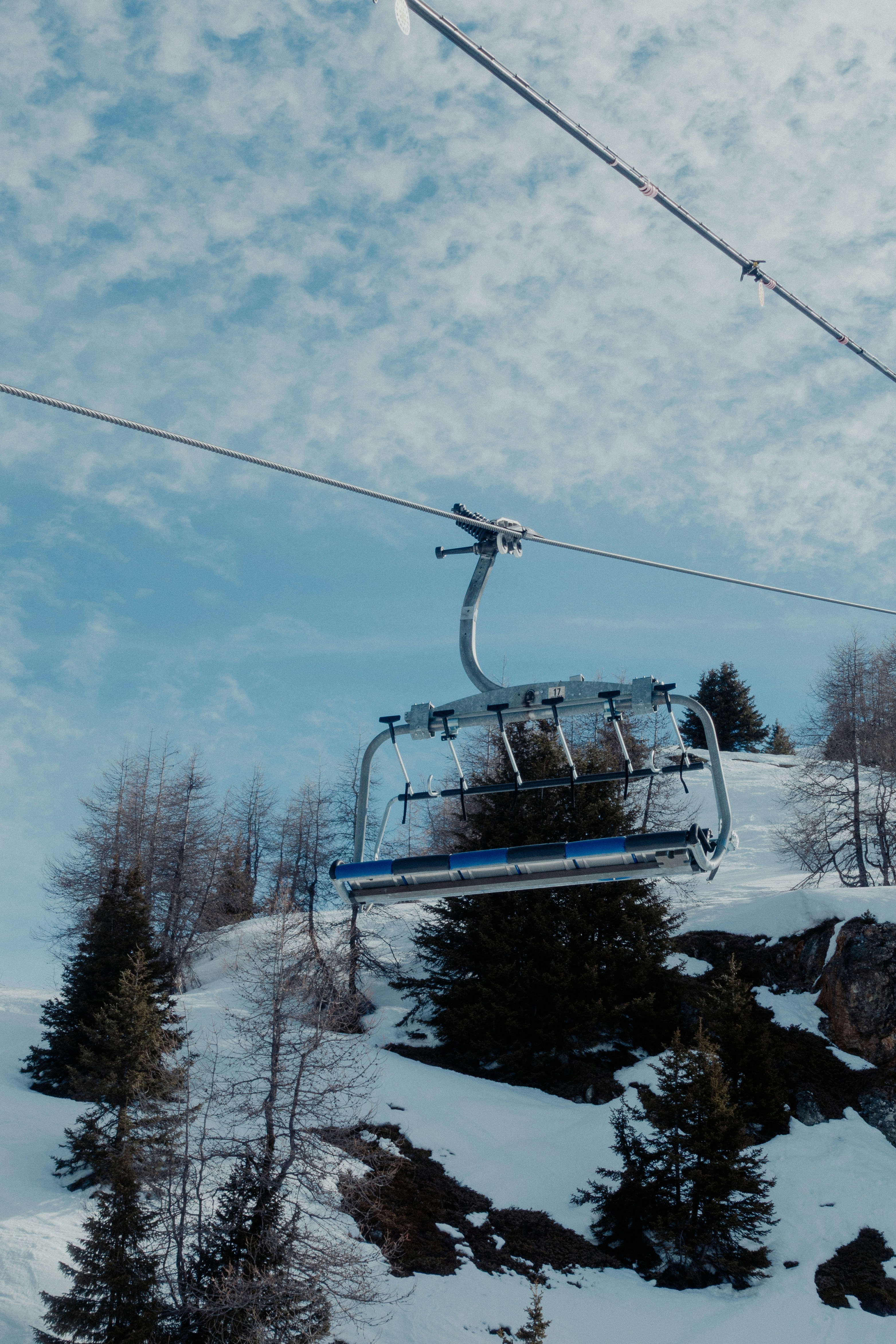 Chairlift car drifts above snow with trees and rocky terrain below; clear blue sky enhances the alpine scene. (Logo/illustration not present; photograph captured with depth in landscape).