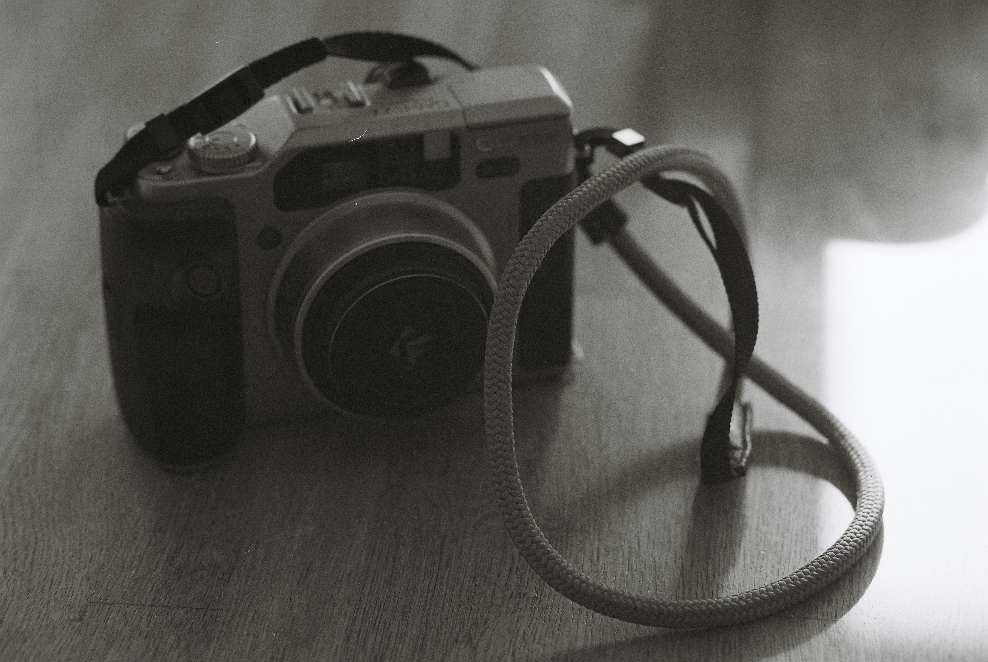 A classic film-era camera rests on a wooden table, its strap casually looped nearby, conveying a scene of timeless photography practice.