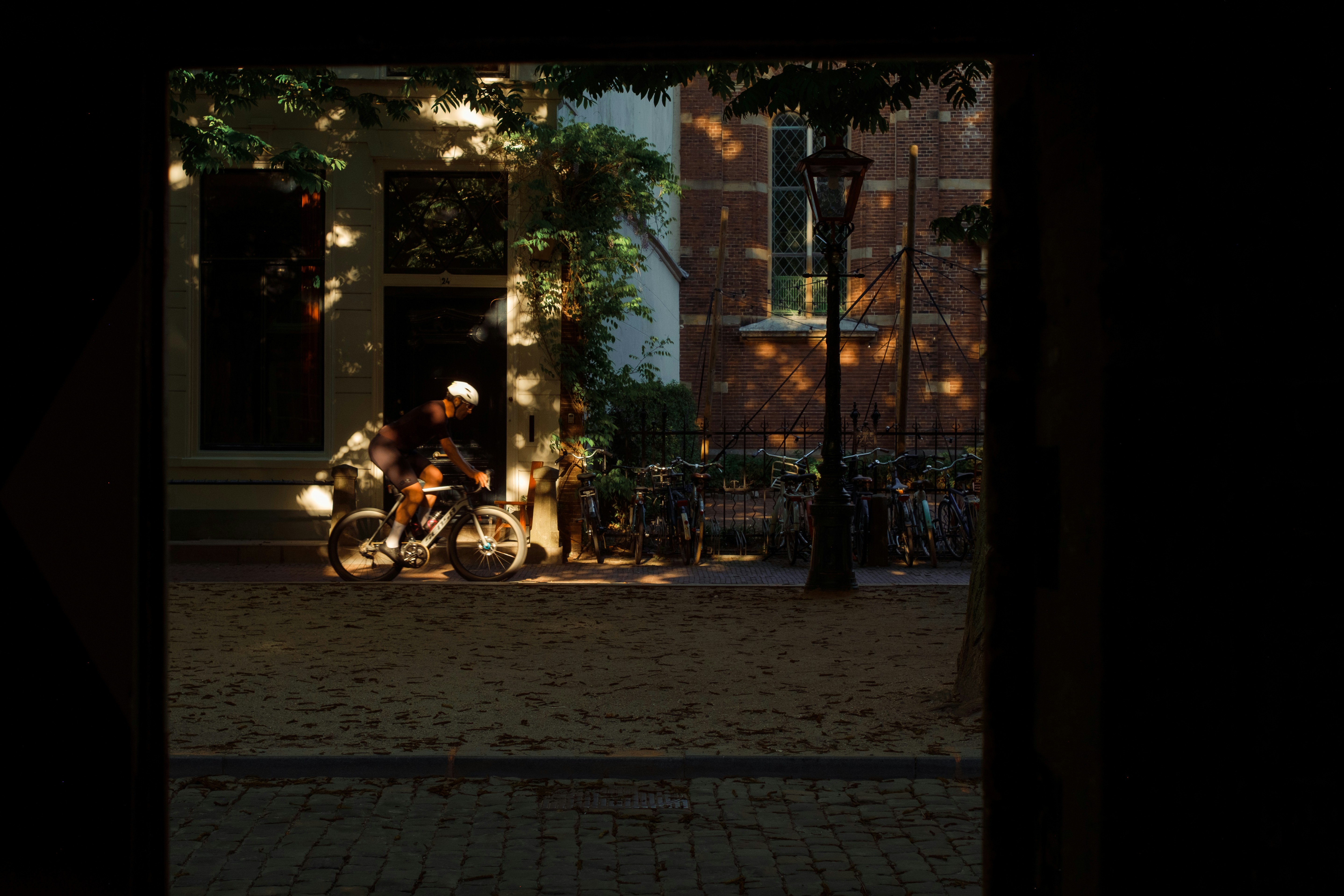 A cyclist captured through a dark archway riding along a sun-dappled street with classic Dutch architecture in Leiden, Netherlands.