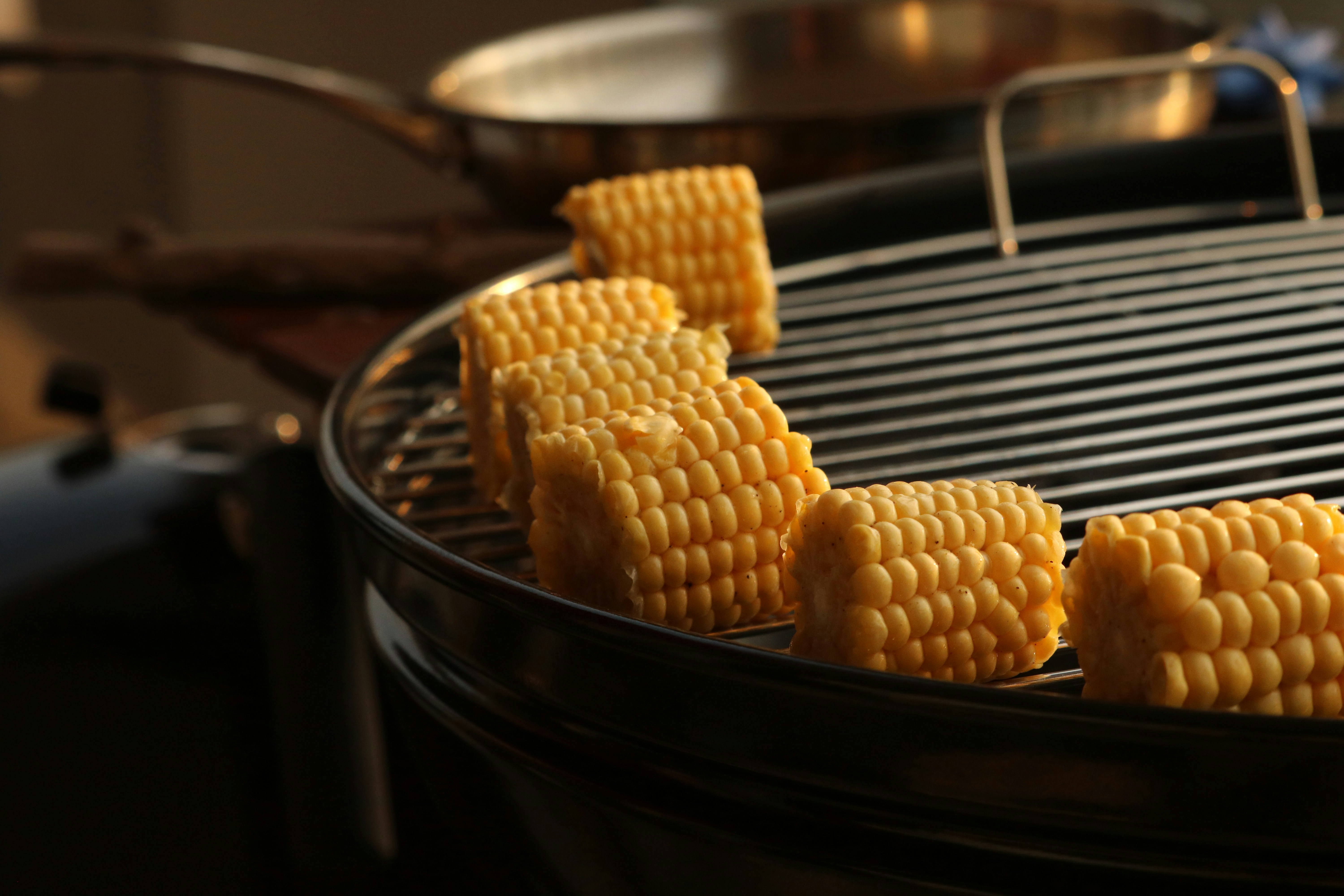 Golden corn on the grill sizzles in a dark skillet, suggesting a warm, intimate kitchen grilling scene.