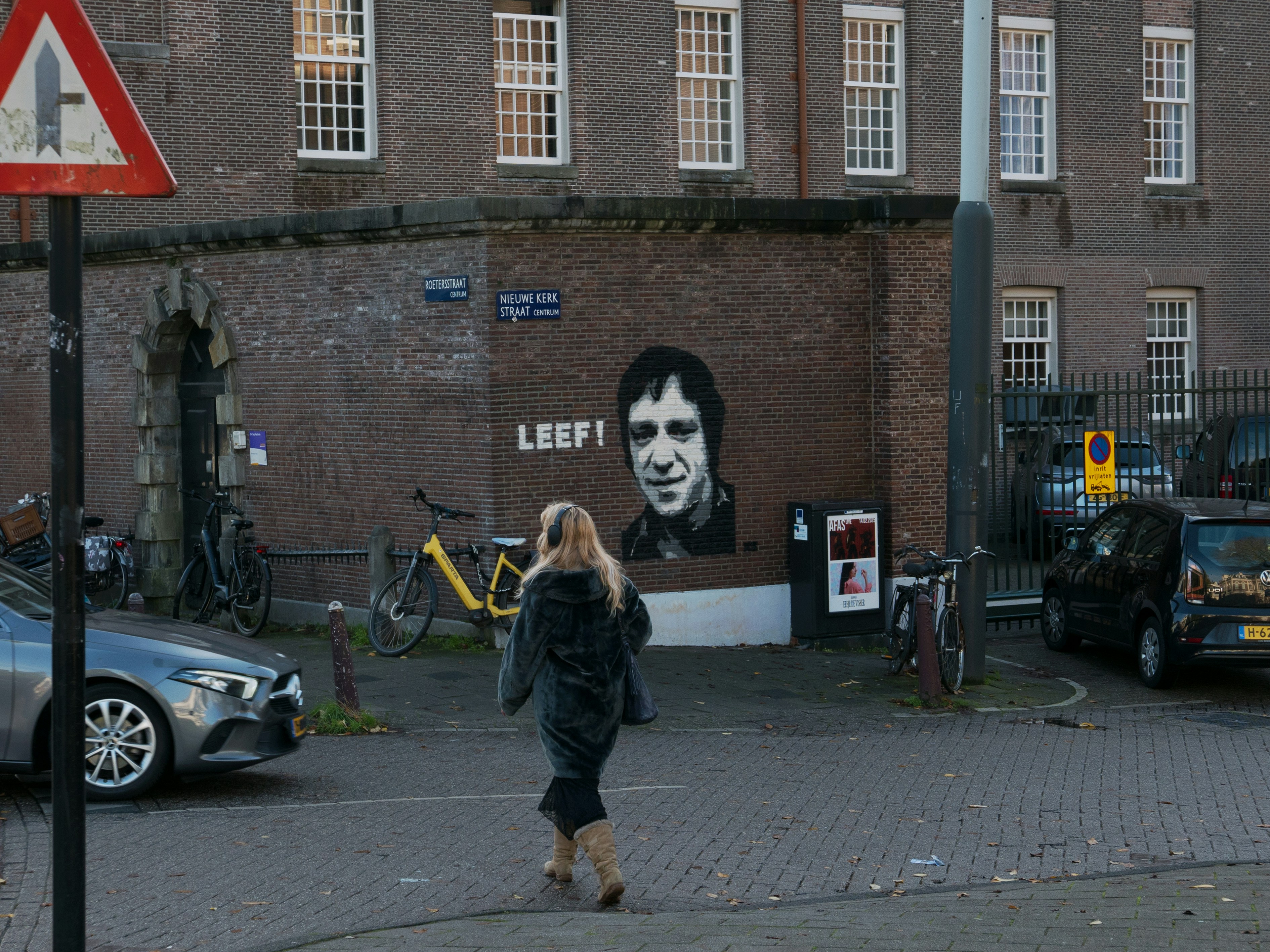 Portrait Wall: A Woman Walks Past Street Art in a Quiet Danish-tinged Square