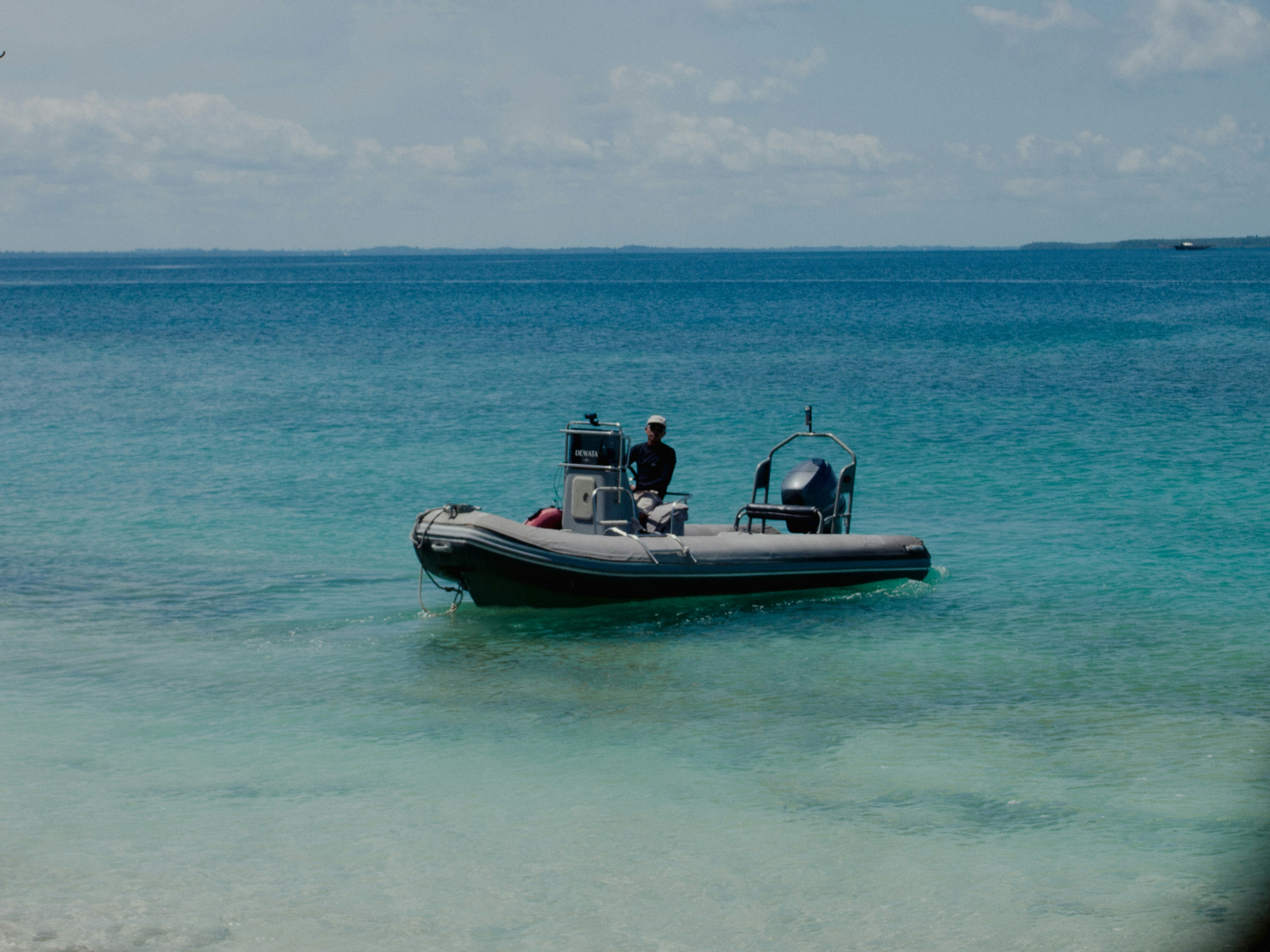 A small inflatable boat rests near the shore in turquoise water with a distant horizon and a clear blue sky.