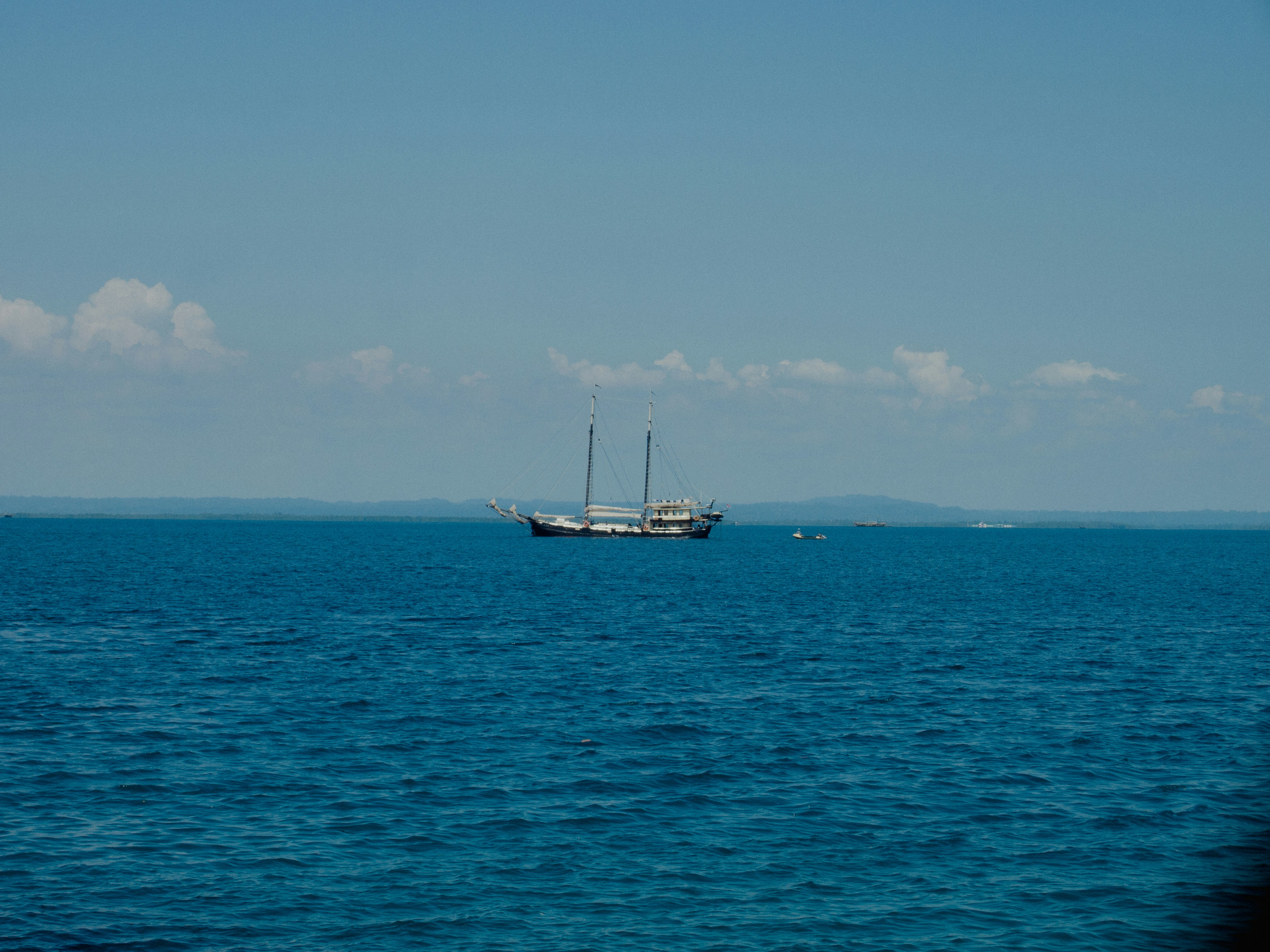 A lone sailing boat rests on a tranquil blue sea under a clear sky, with distant land on the horizon; a simple seascape conveying openness and calm.