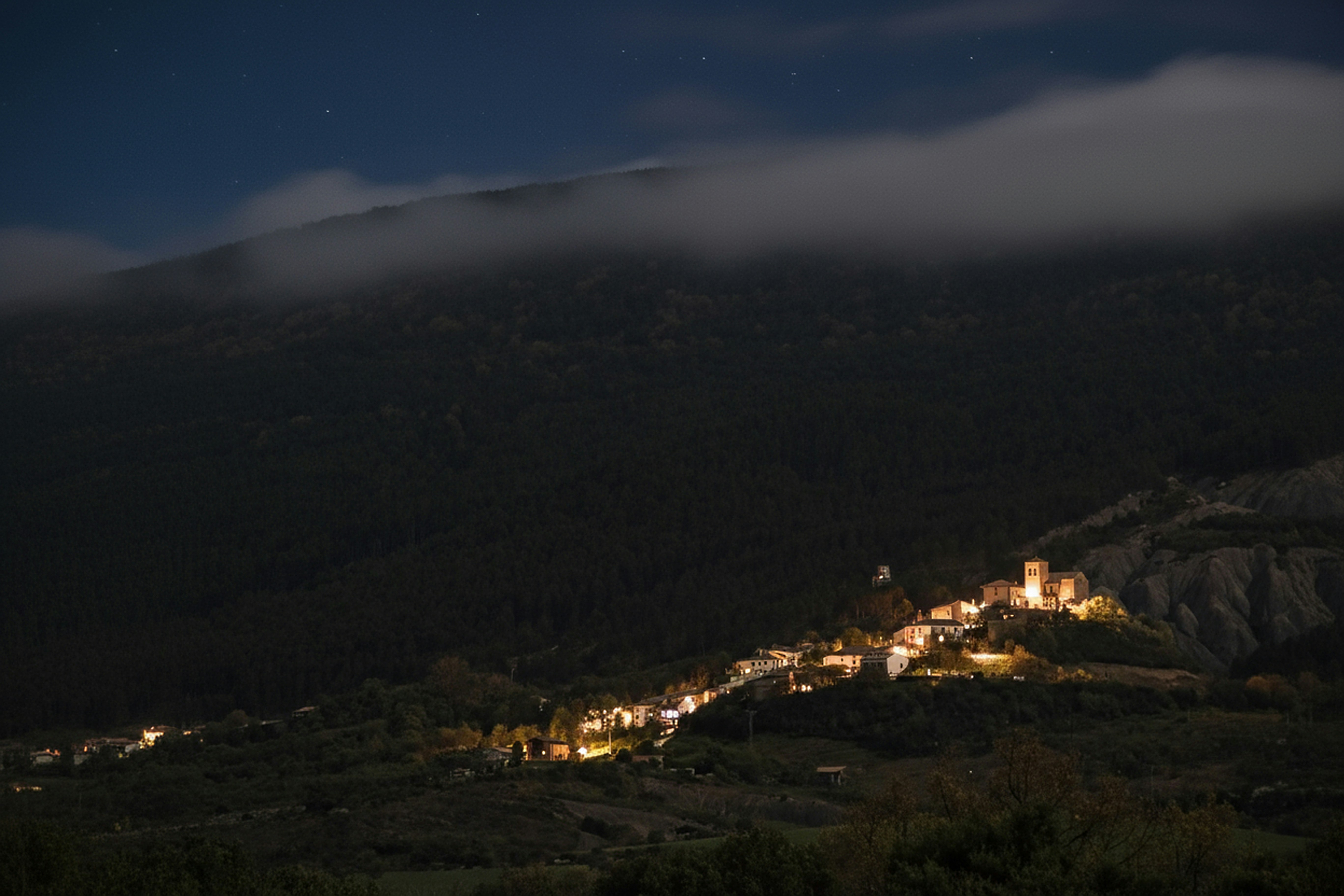 Moonlit hillside village under a drifting cloud