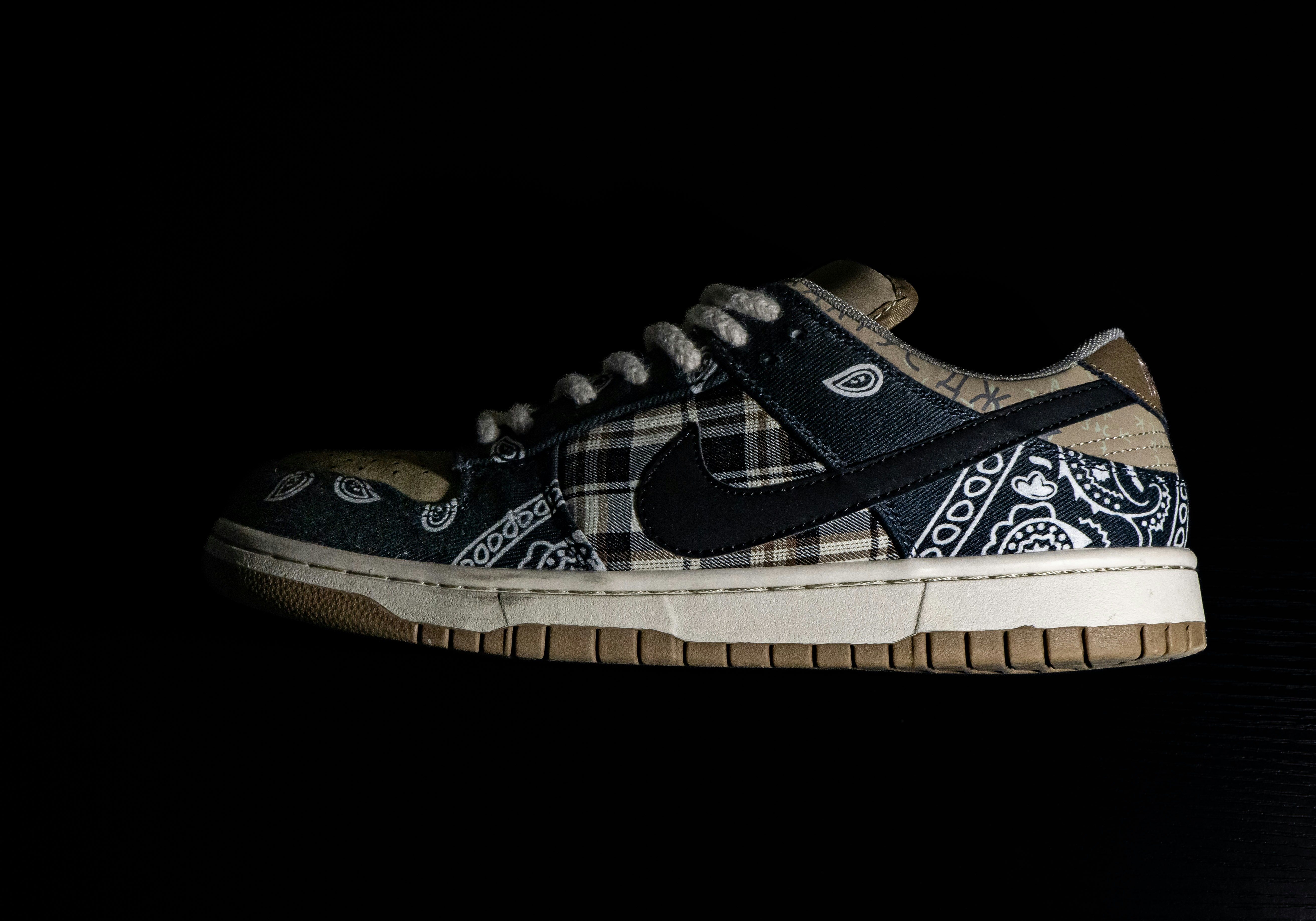 Bandana-pattern low-top sneaker rests on a dark background with dramatic sidelighting, highlighting texture and contrast. This is a product-style shot focusing on design details and materials.