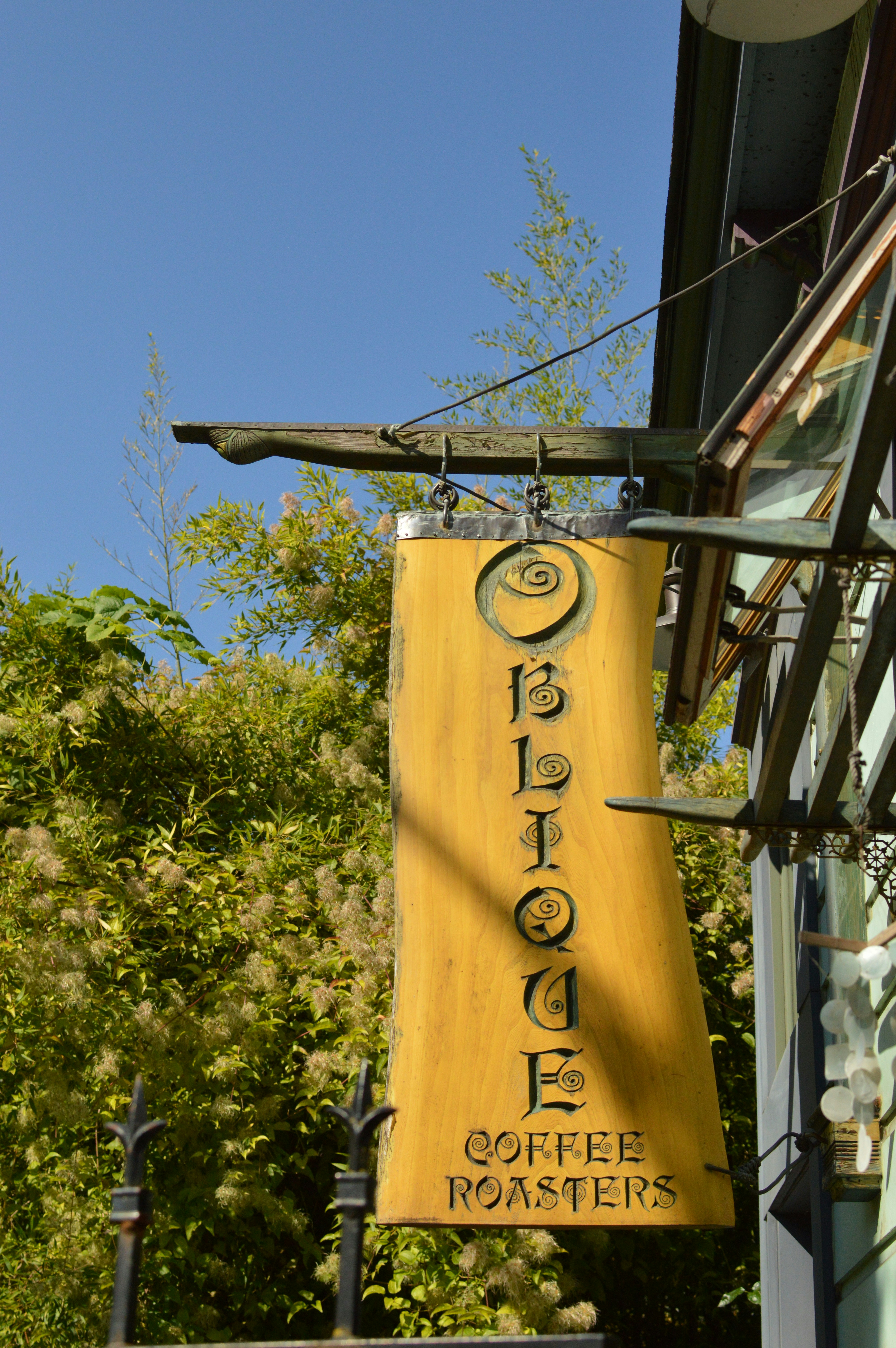 Vertical signboard of a coffee roastery catches the sunlit storefront amid lush greenery