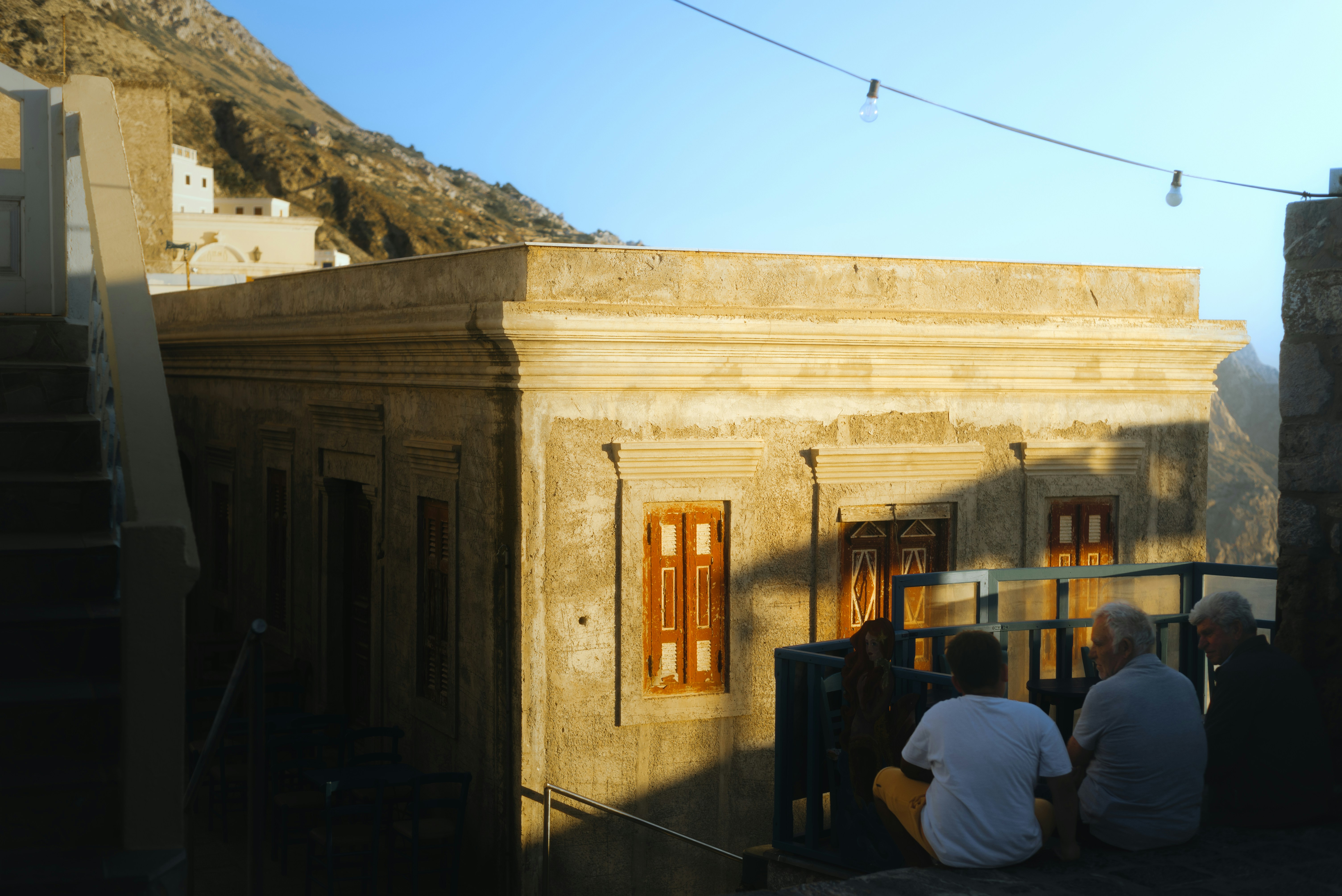Sunlit Stone Facade and Conversing Tourists on a Cliffside Terrace