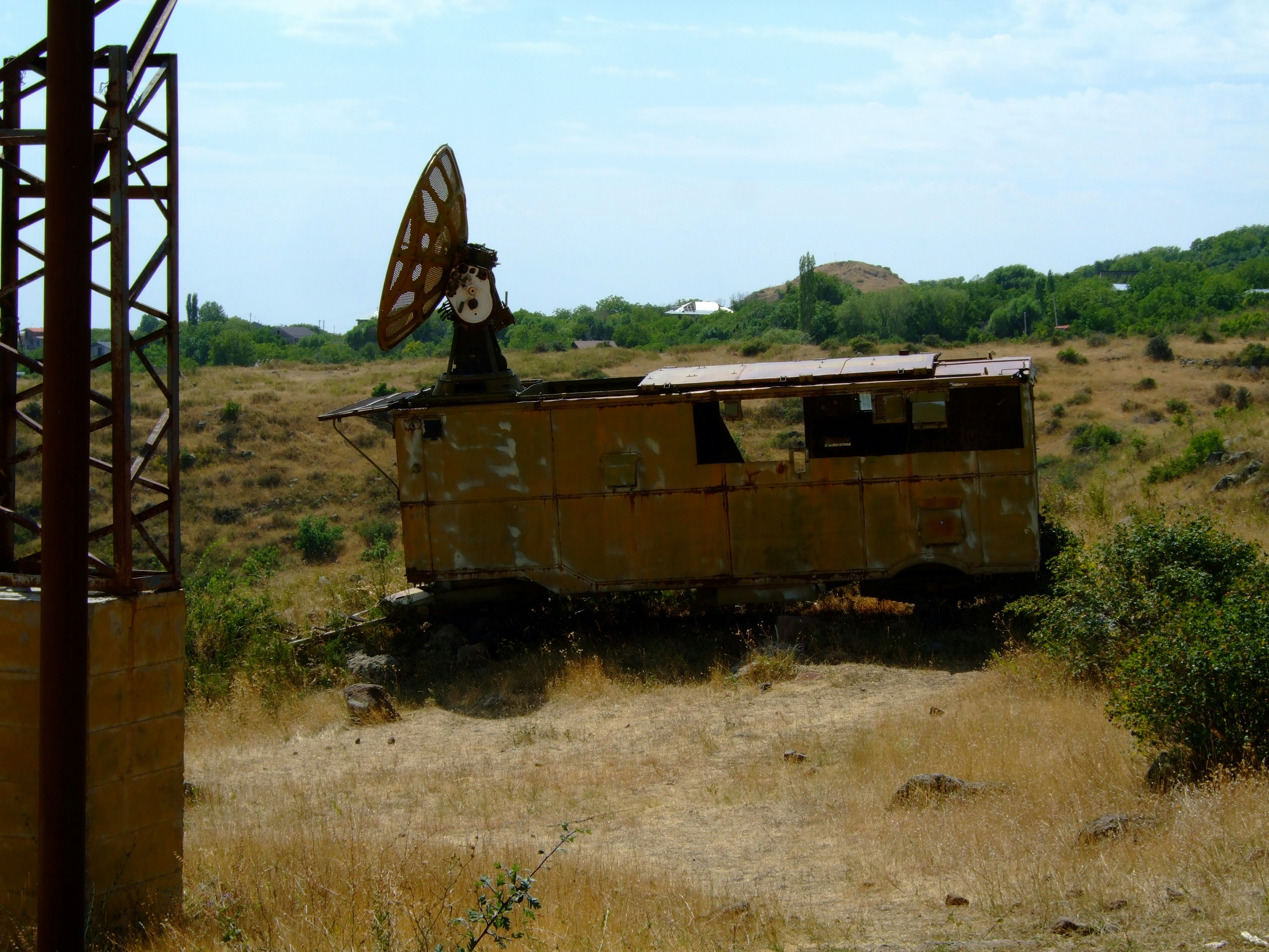 A rusted mobile radar unit in a dry grassy field under a blue sky