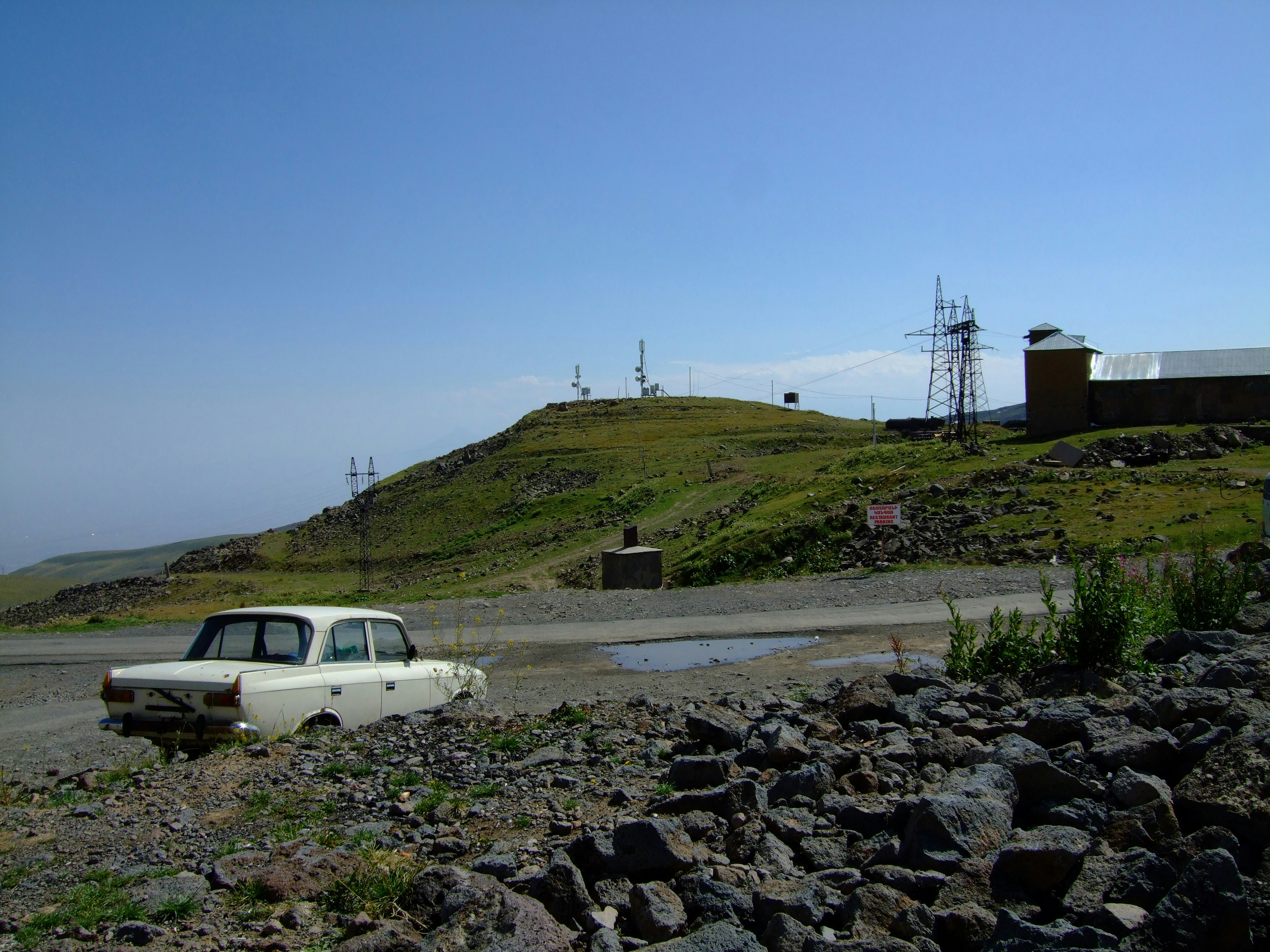 A white vintage car parked on a rocky roadside near a grassy hill