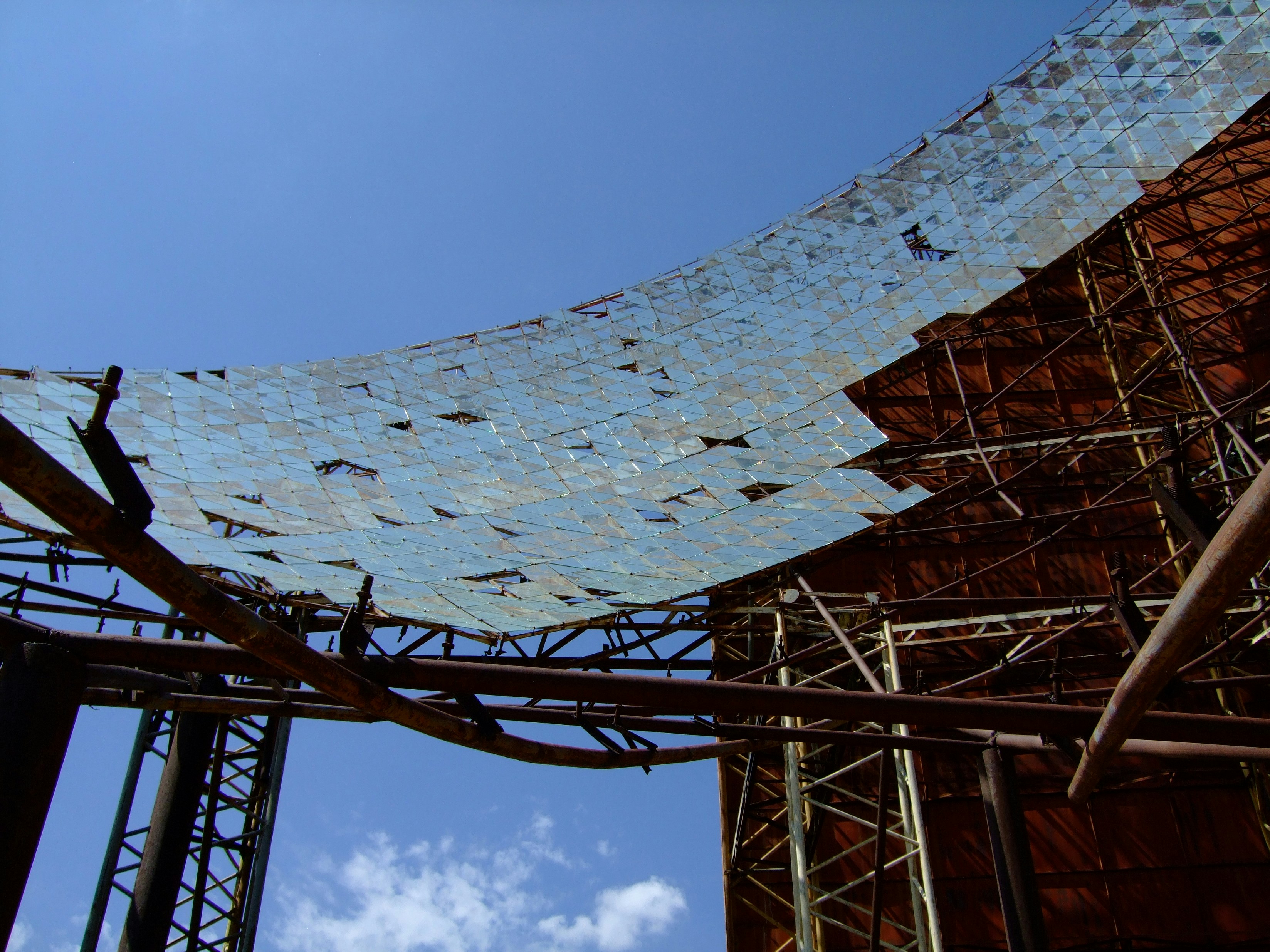A large curved array of reflective glass panels on a rusted metal frame