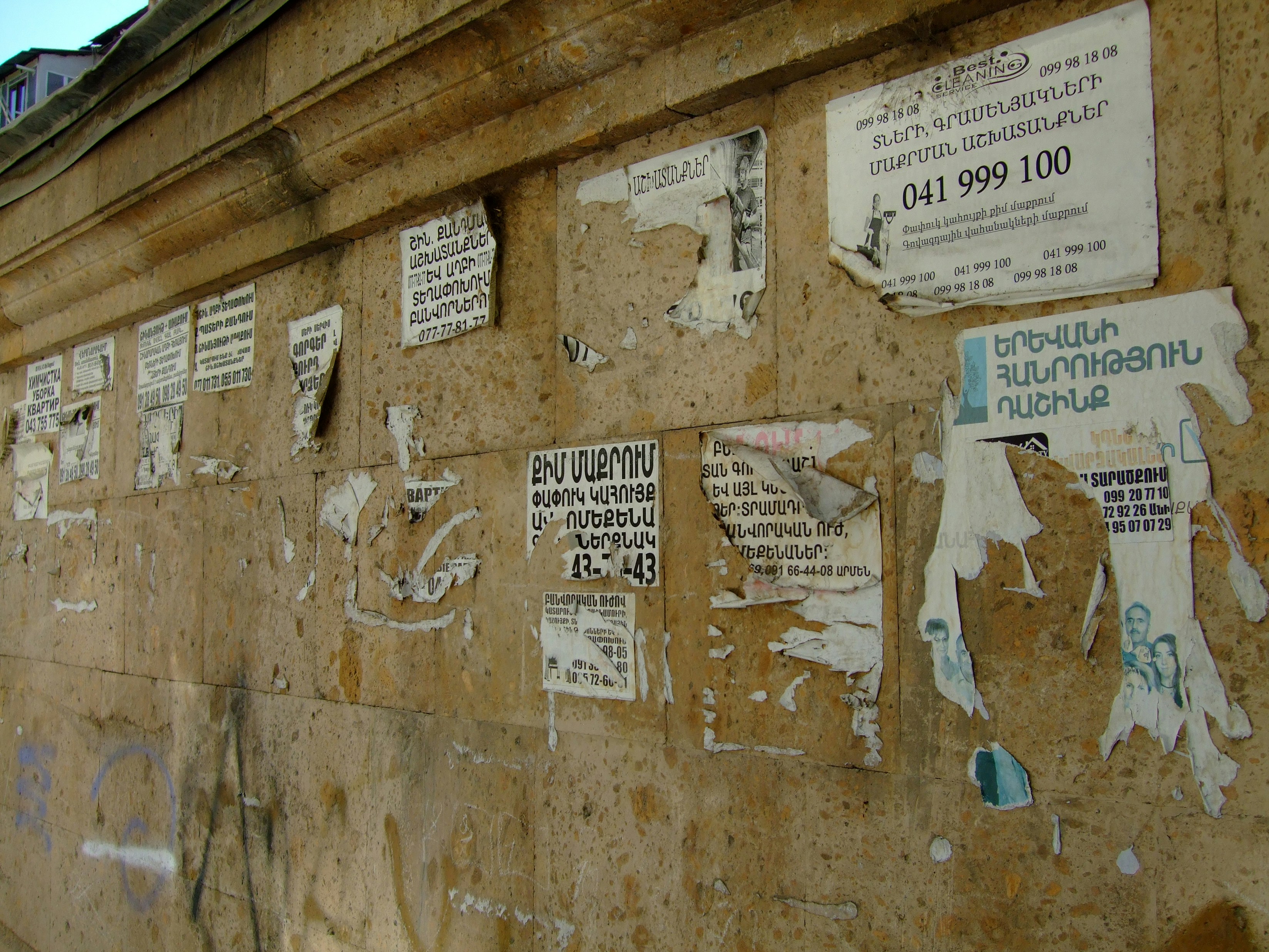 Torn paper advertisements on a weathered stone wall in an urban setting