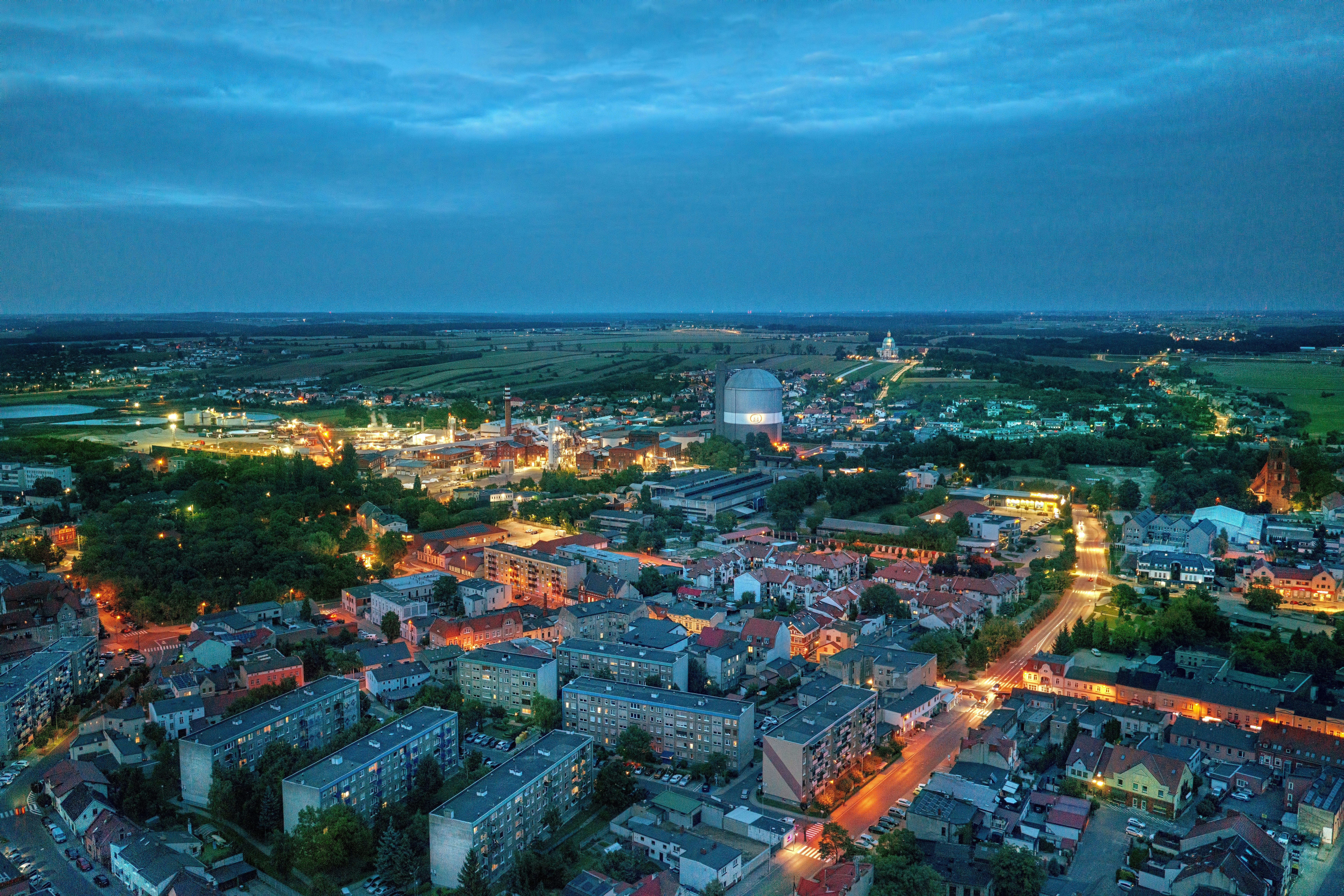 Aerial view of a small city at dusk with illuminated streets and a prominent white dome near the center, conveying a calm urban panorama.
