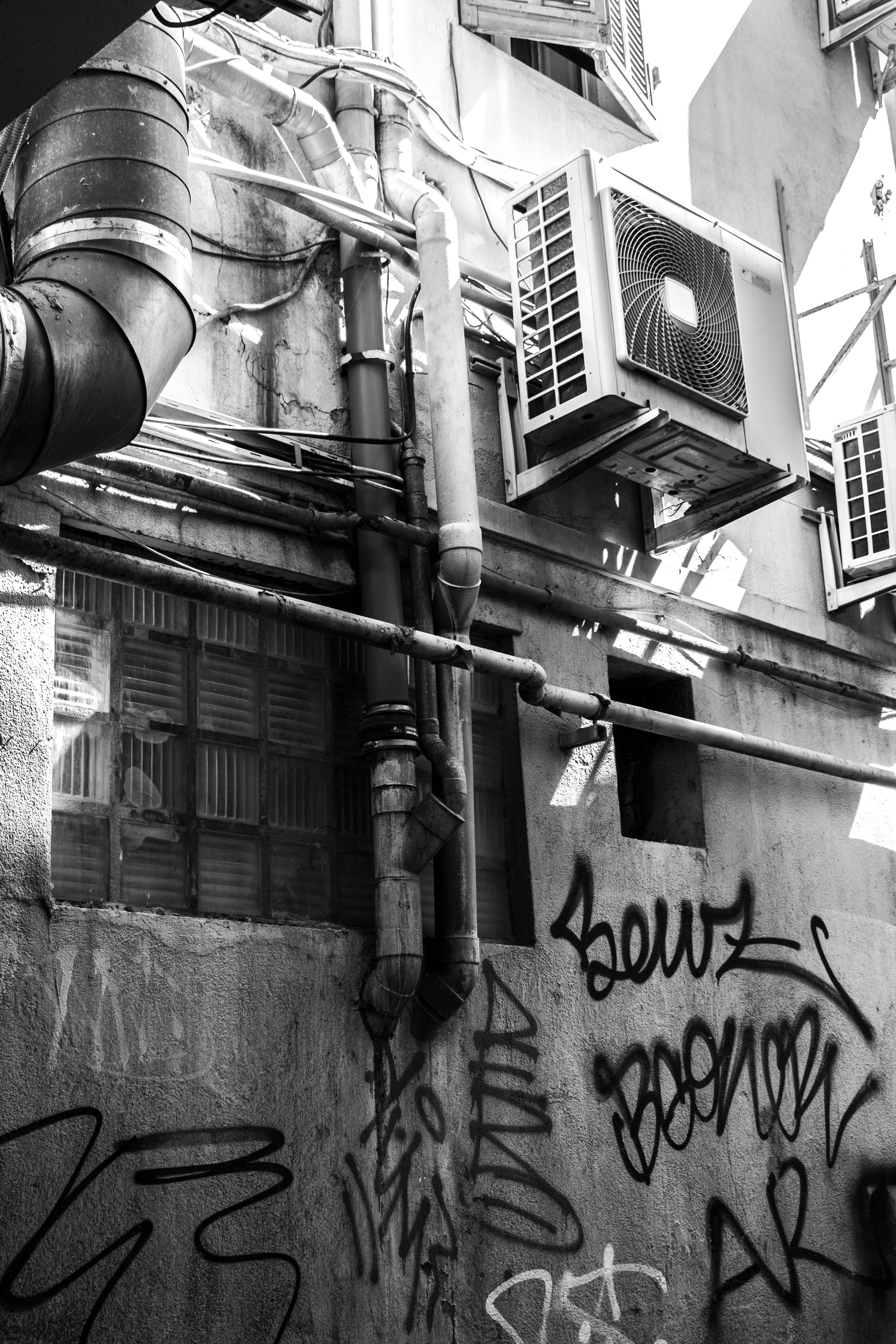 Urban machinery: tangled pipes and graffiti under the air conditioner