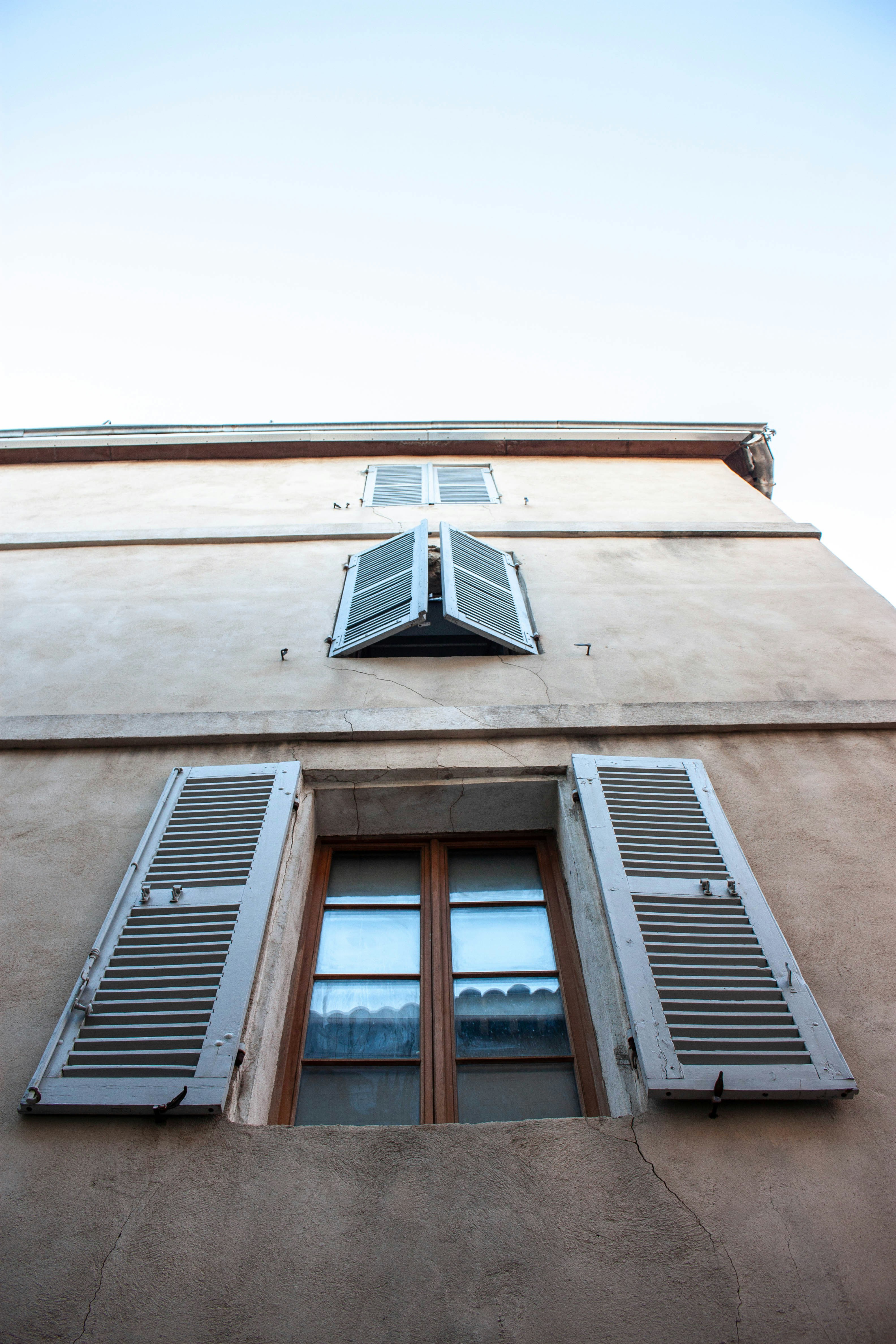 Windowed Facade: A Sunlit House with Weathered Shutters