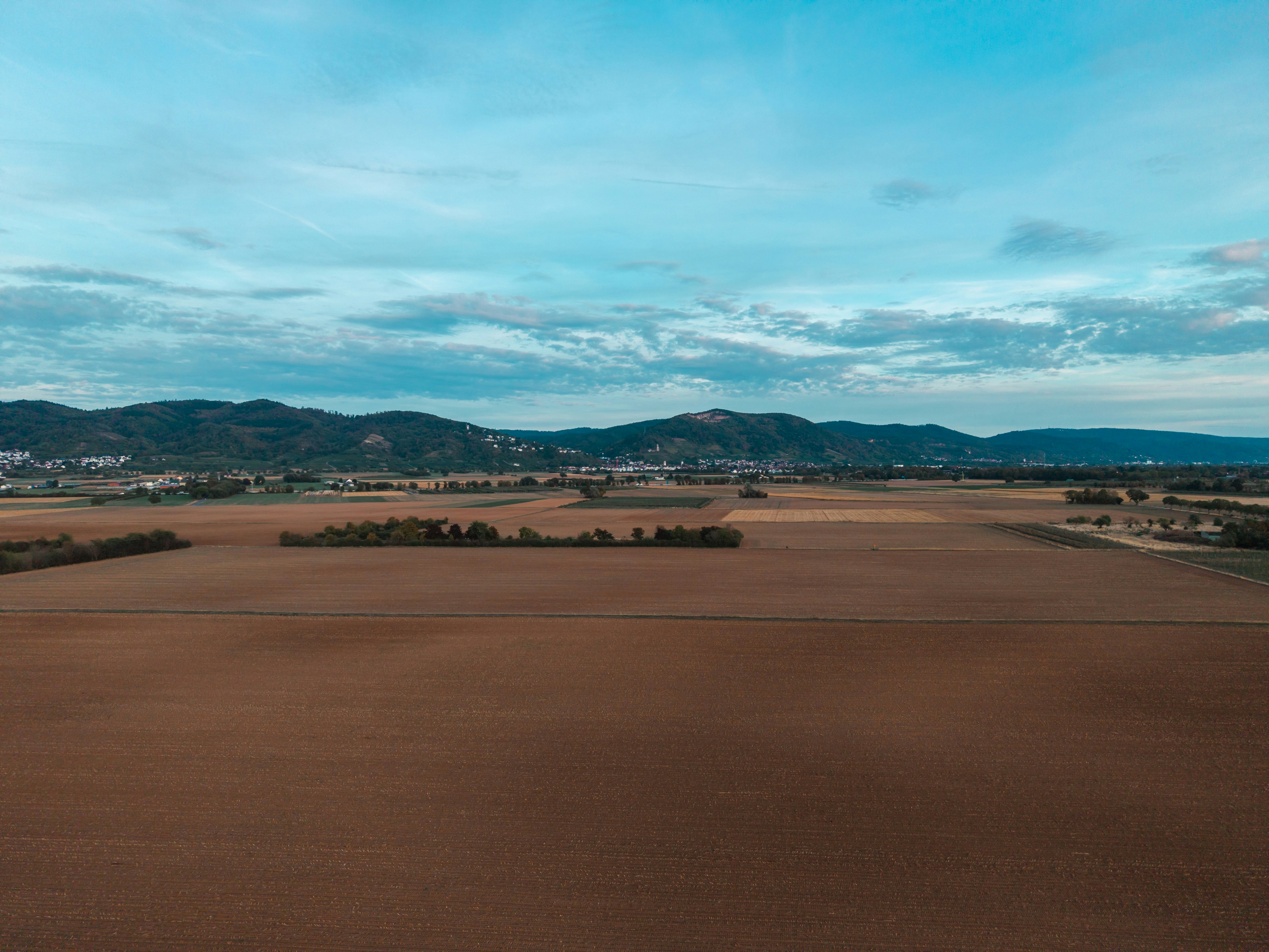 Expansive farmland under a blue sky with distant hills, a calm, wide-angle landscape capturing open fields and subtle cloud drama.