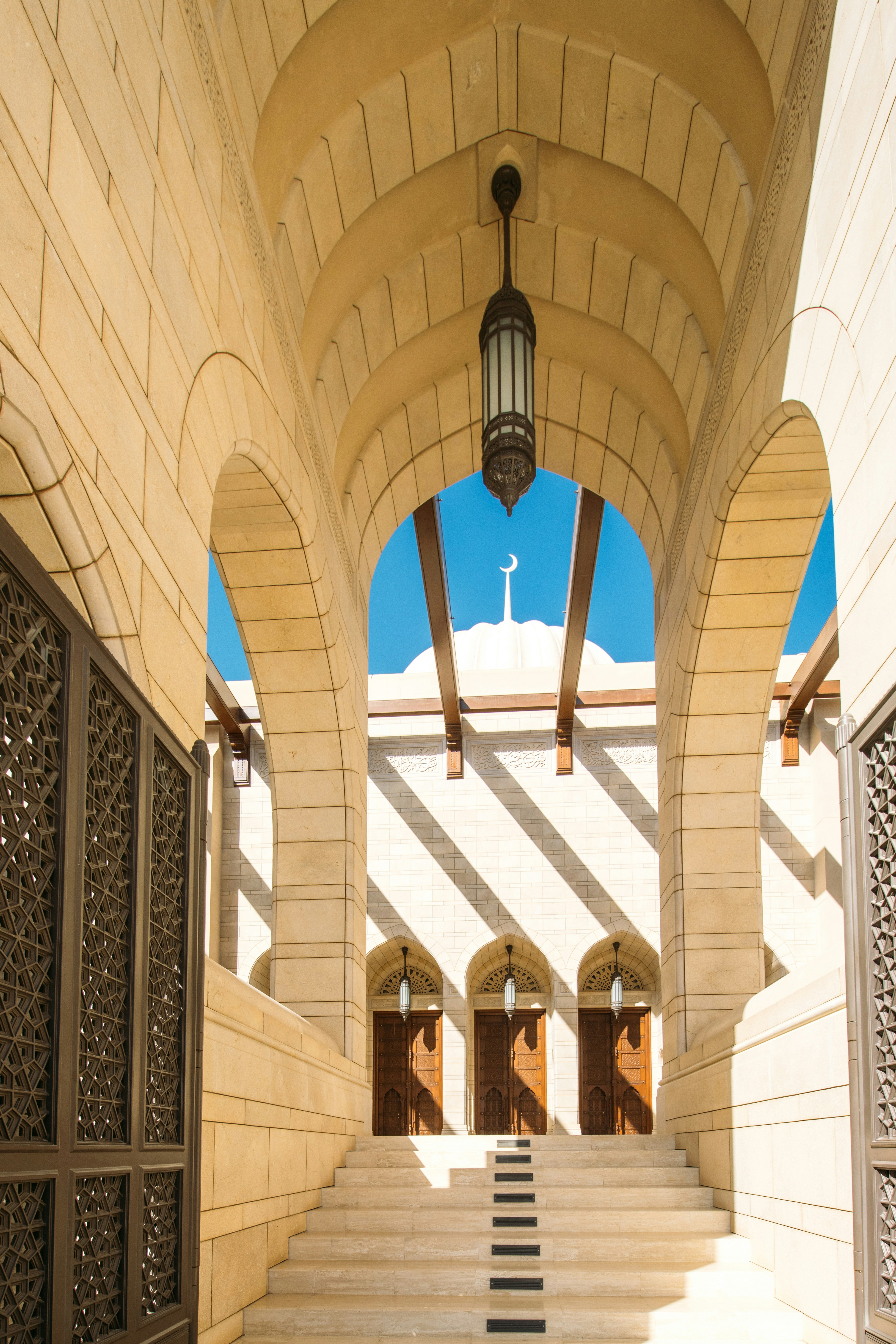 Stone arches leading to a mosque courtyard with a white dome and crescent