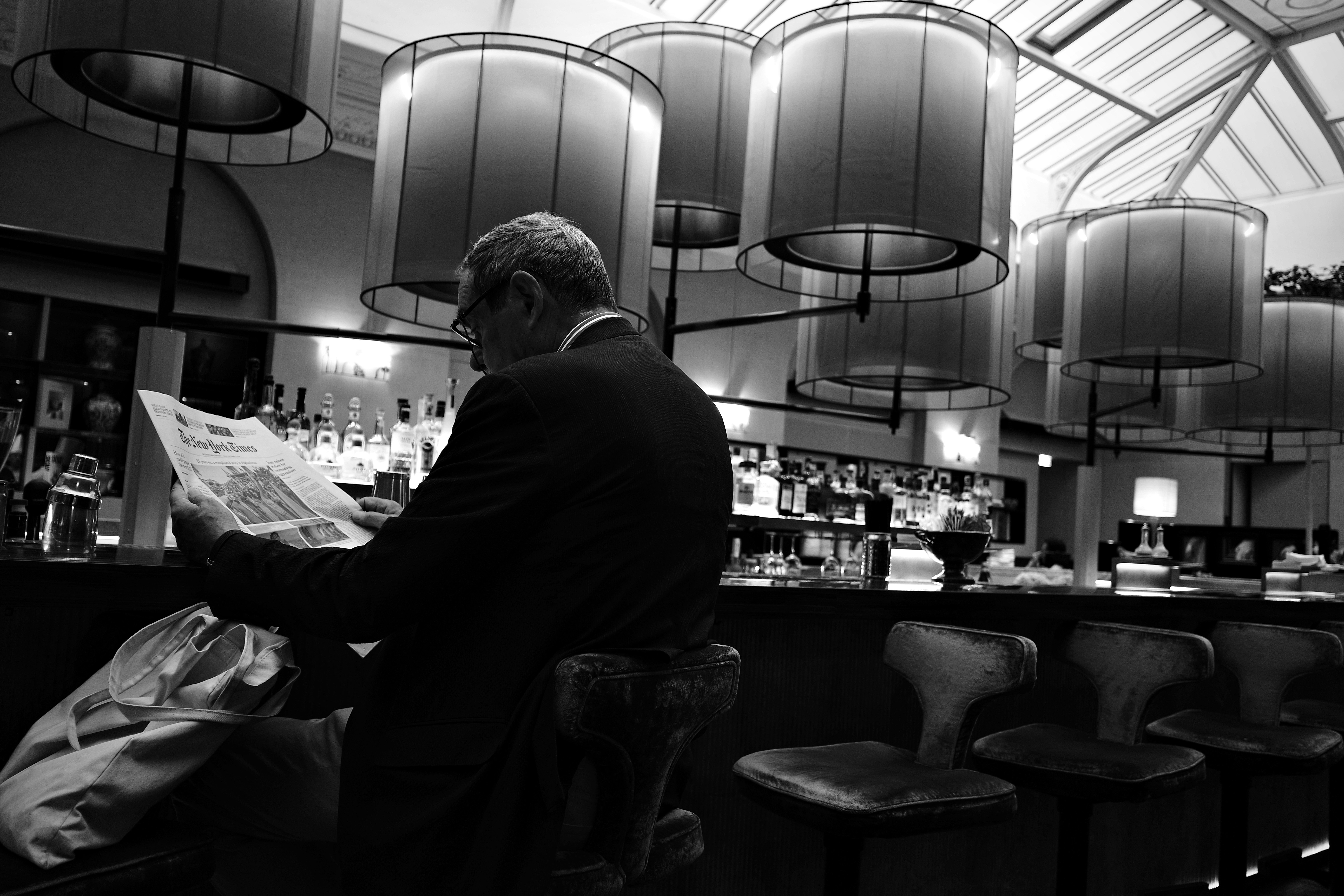 Man in suit reads a newspaper at a dimly lit bar