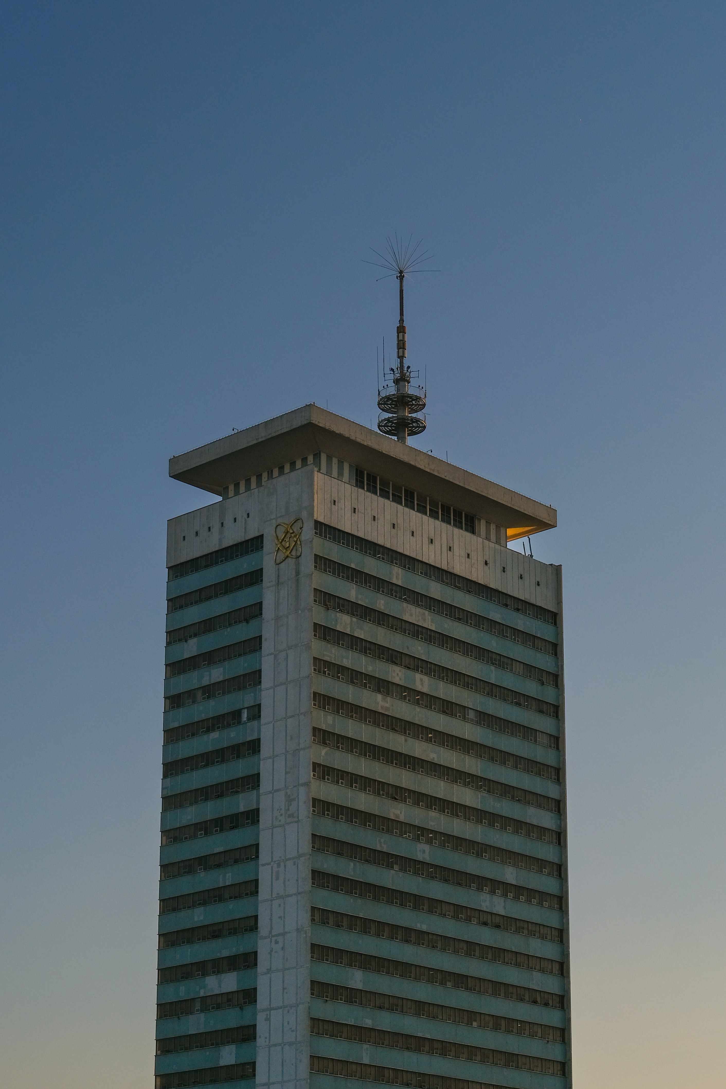 Mid-rise tower with a prominent antenna array rises against a clear blue sky, emphasizing architectural lines and the top communications mast.
