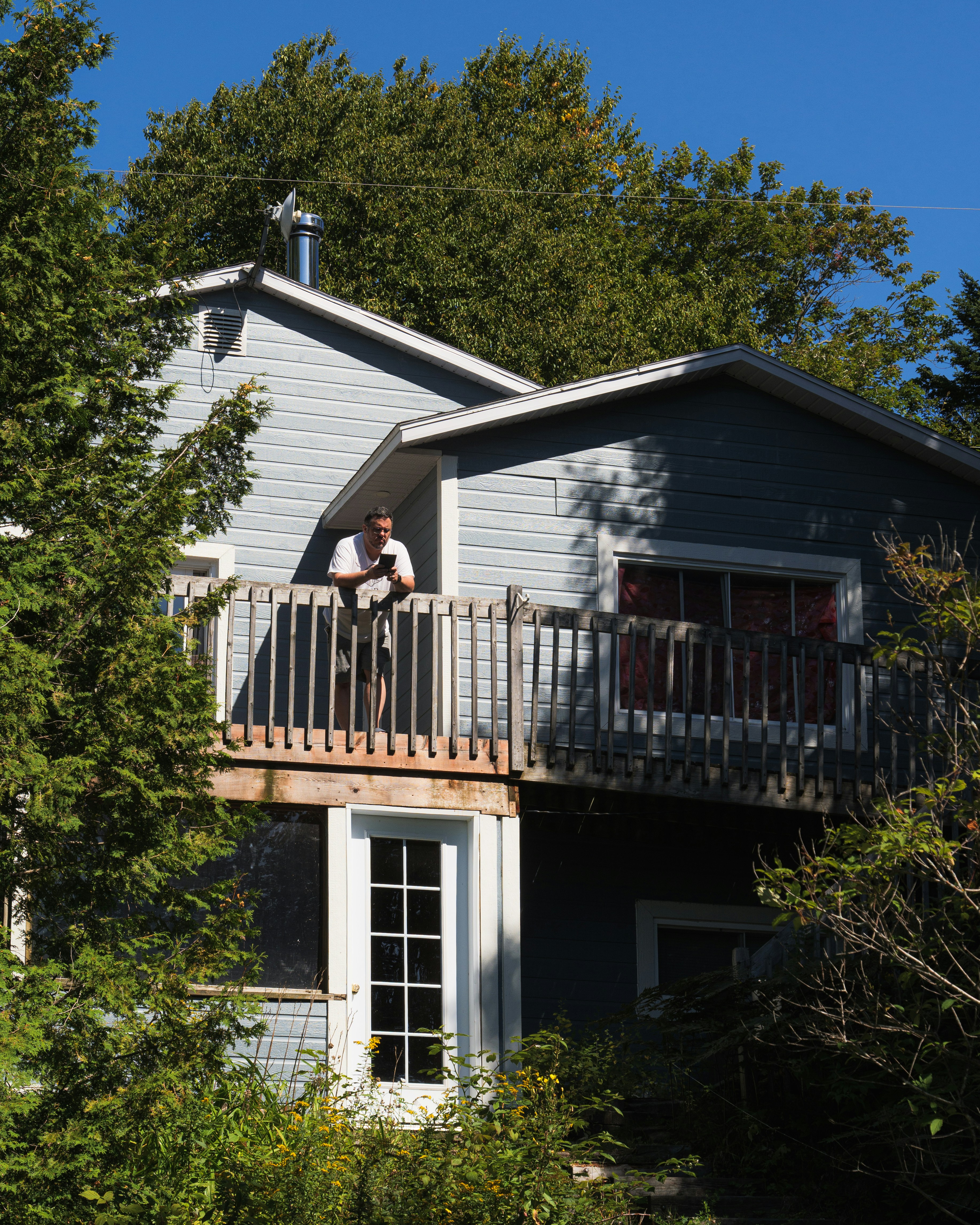 Balcony Vigil: A Man Watches from a Quiet Blue House