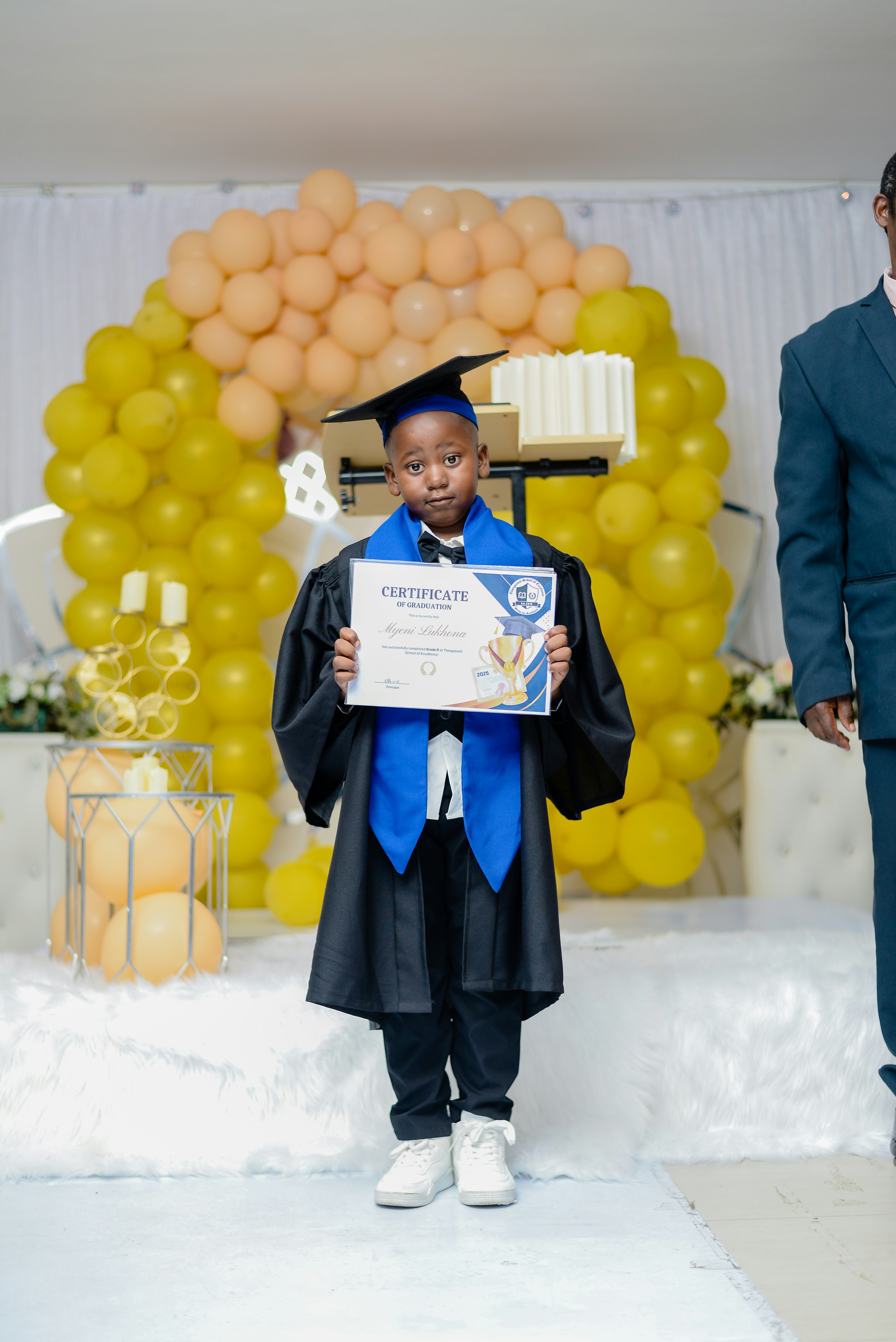 Graduation Joy: A Young Graduate Holds His Certificate Against a Ballooned Backdrop