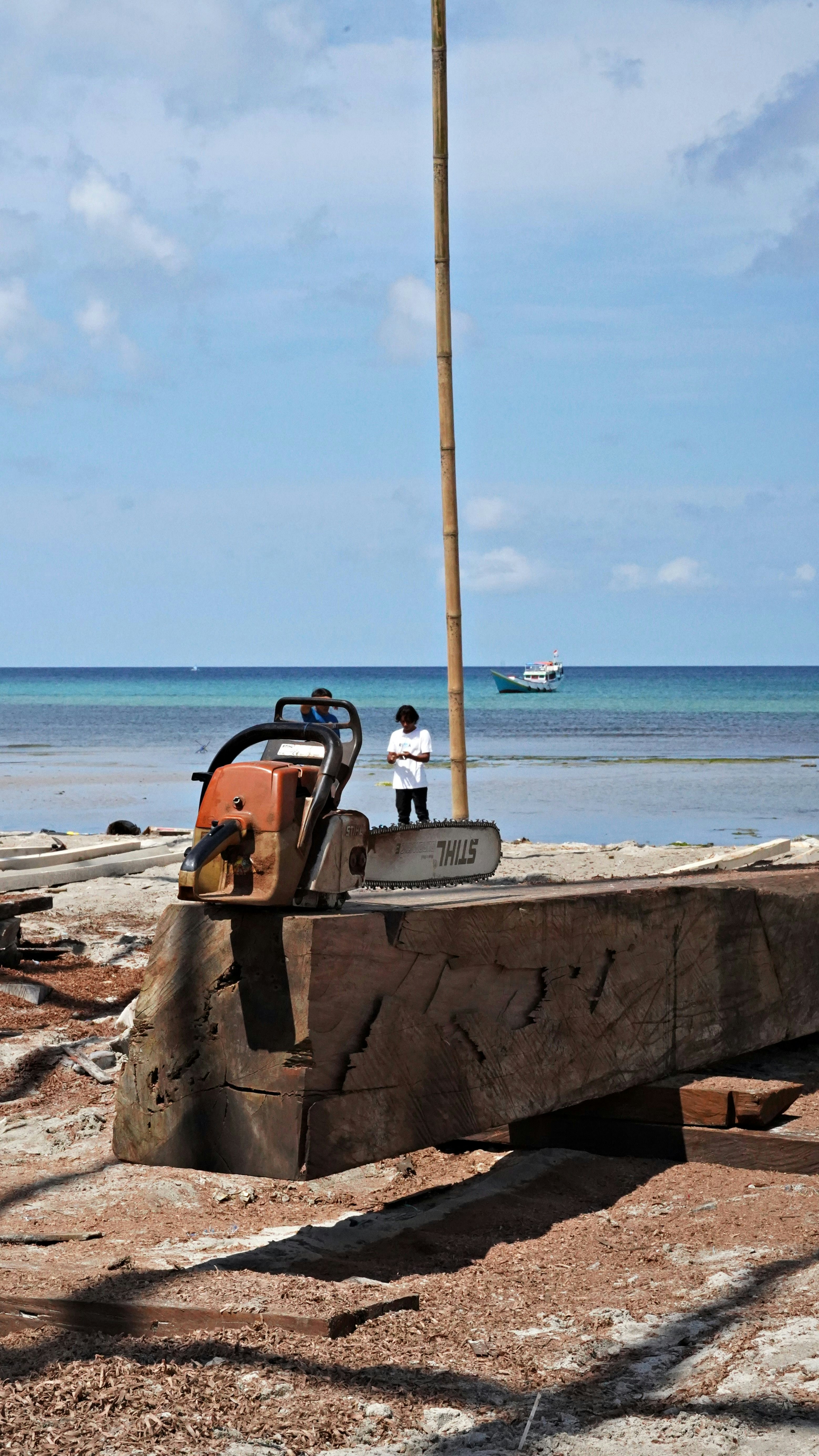 Harbor Idle: Chainsaw, Log and Sailboat Under a Clear Sky