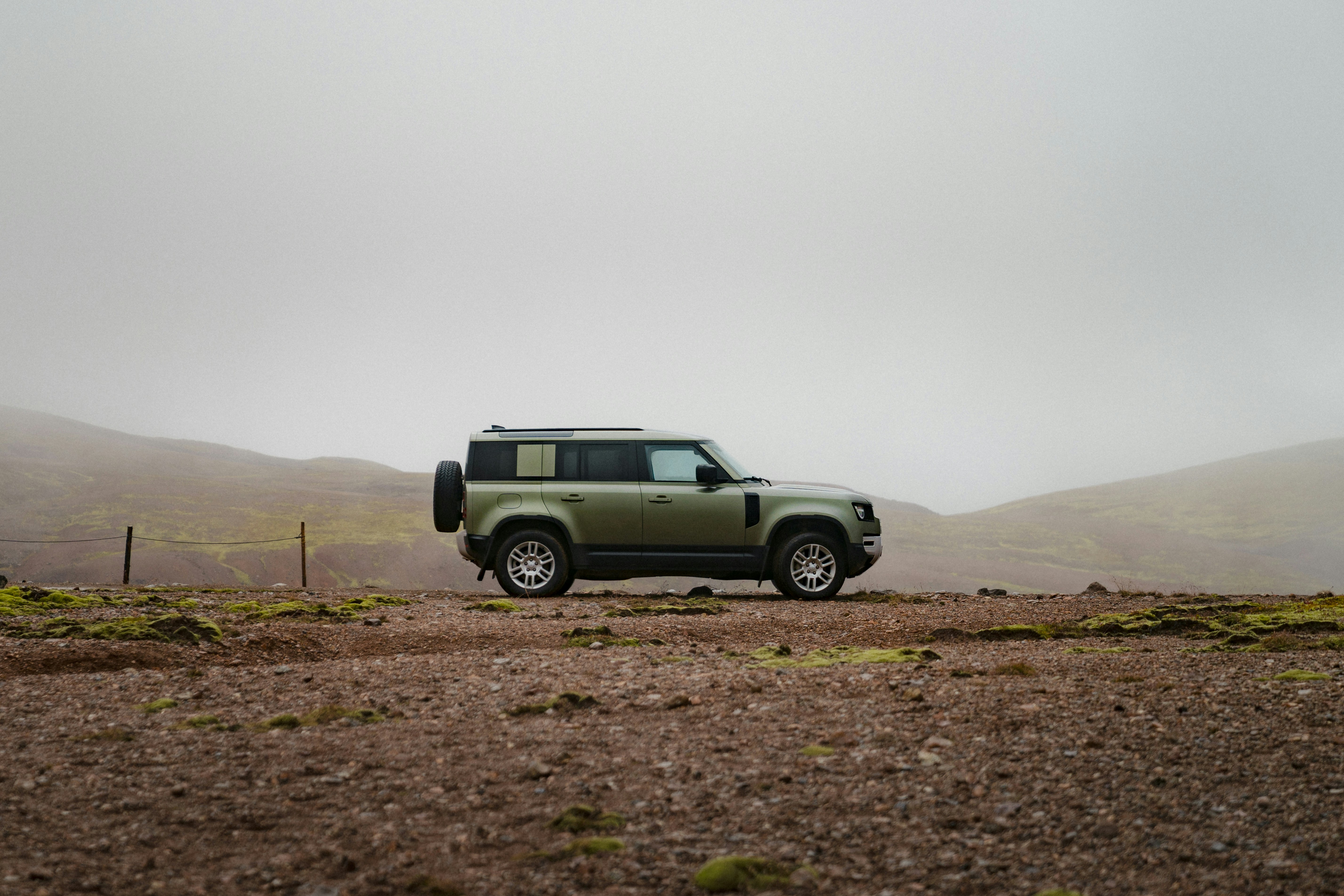Green SUV on a Rugged Highland Road Under Soft Mist
