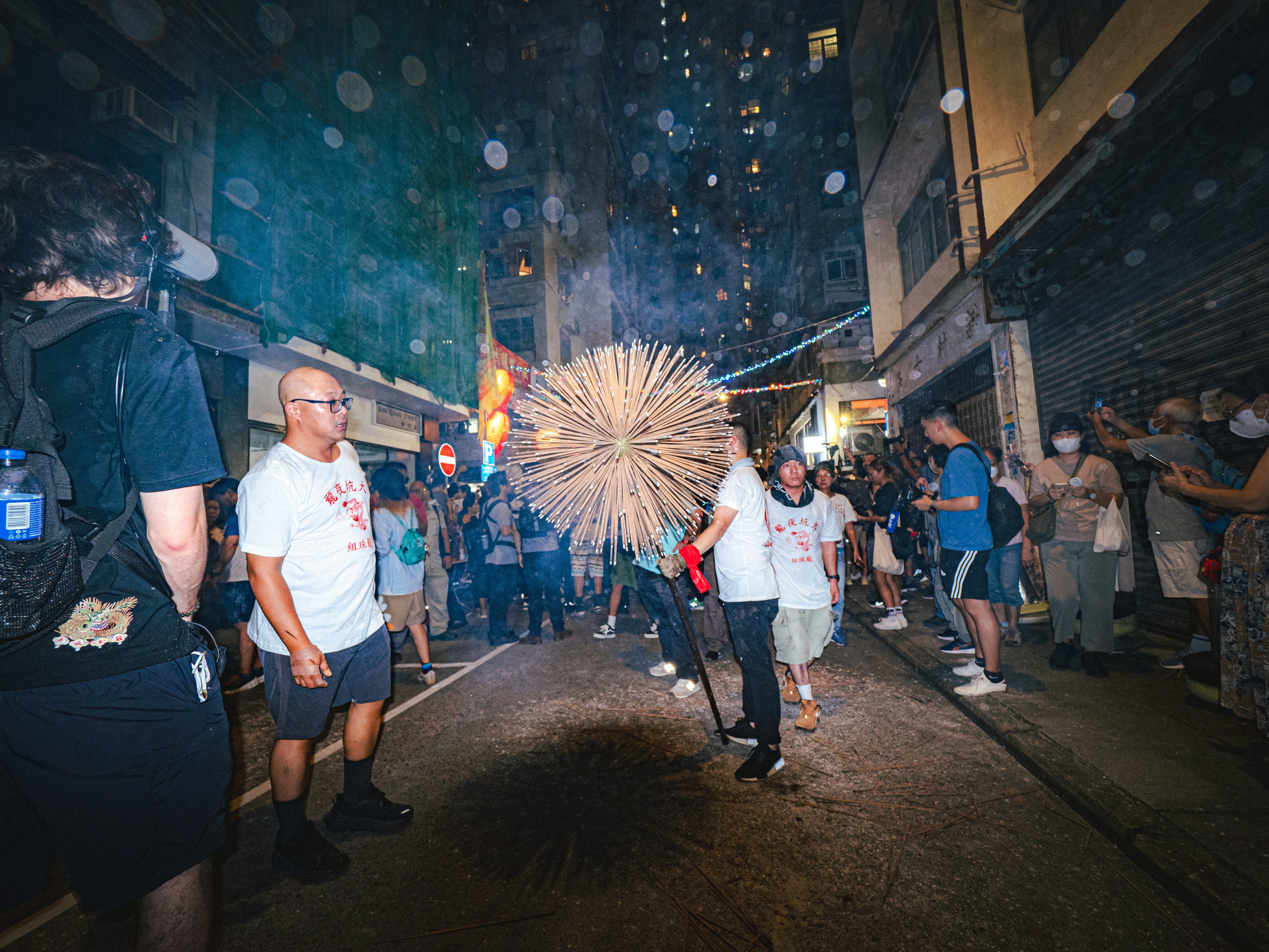 People in a narrow street holding a large spherical incense bundle during a festival