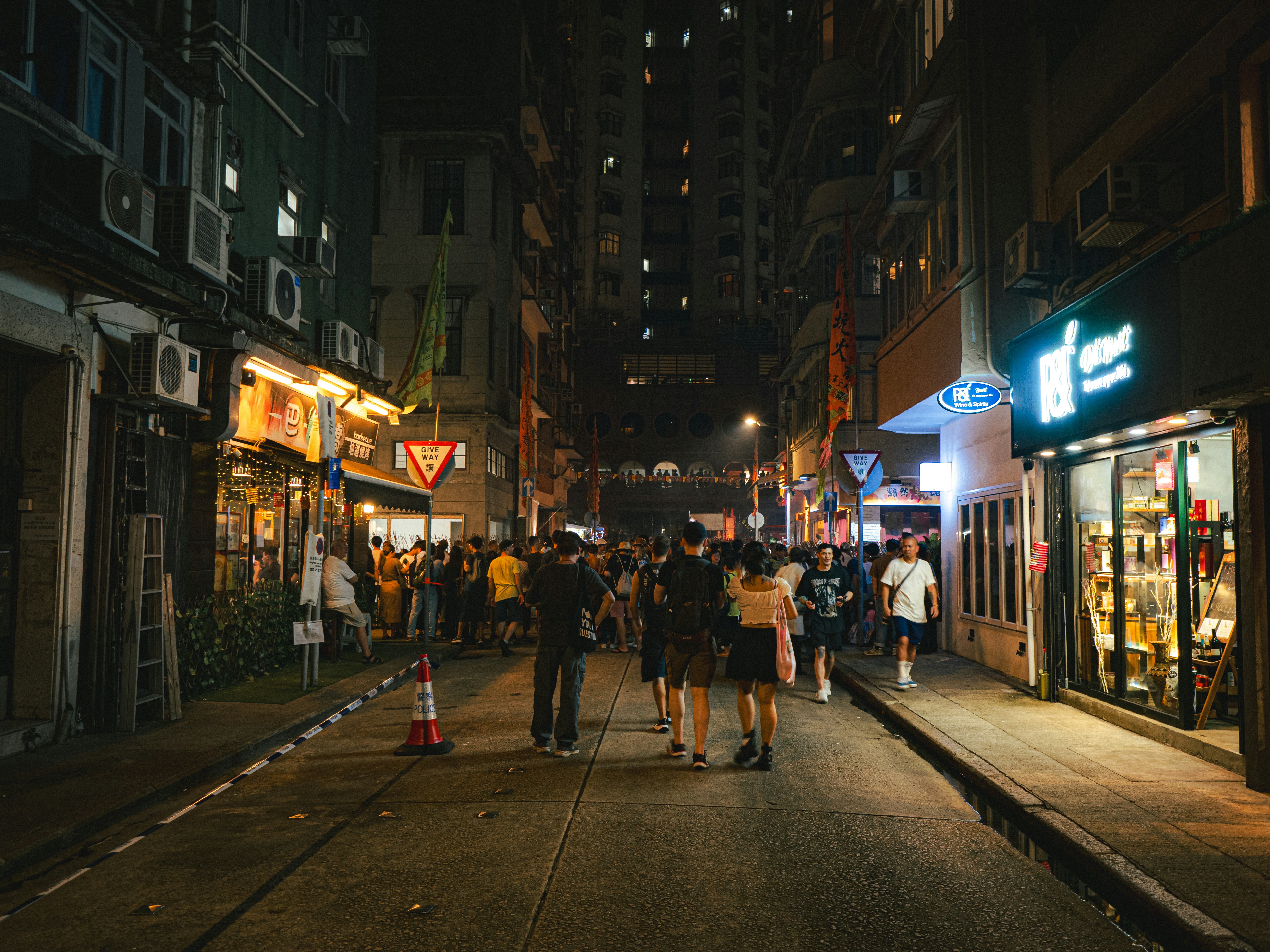 A bustling urban street at night with pedestrians strolling between storefronts and neon signs.