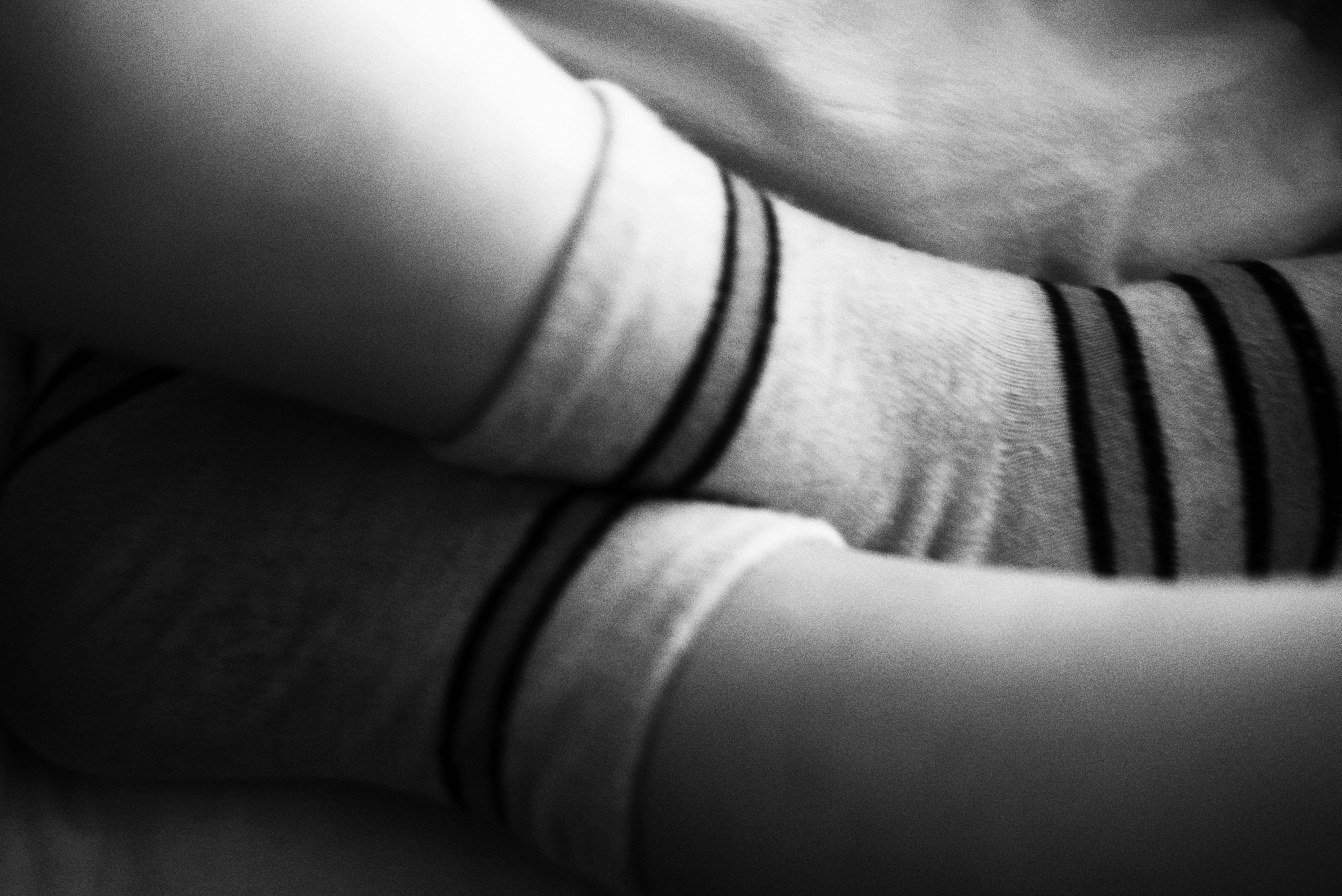 Close-up of layered arms with striped sleeves, rendered in monochrome to emphasize texture and tenderness. A minimal, abstract composition with focus on fabric folds and contrast.