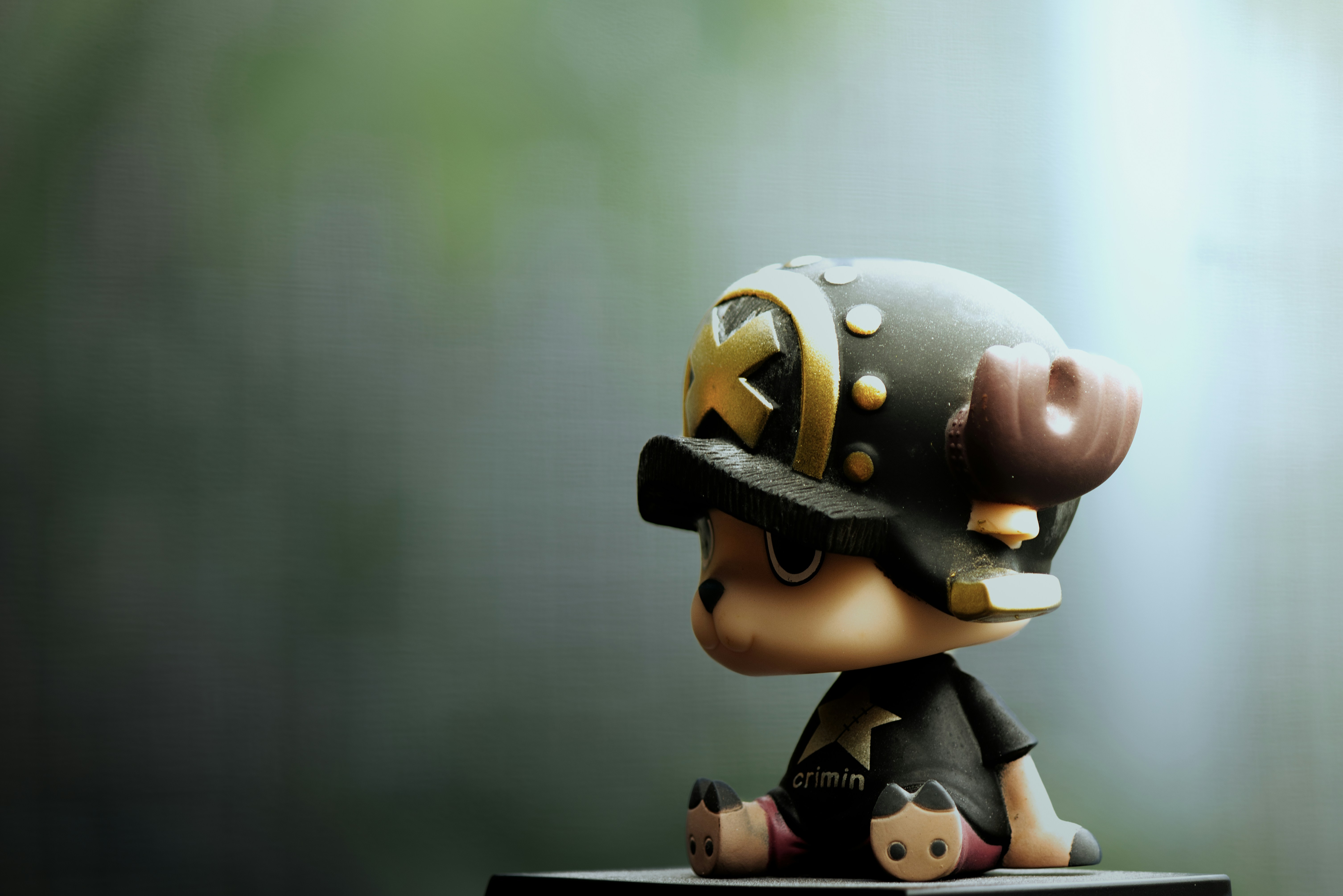 Small figurine wearing a helmet sits on a pedestal with a soft, blurred backdrop.