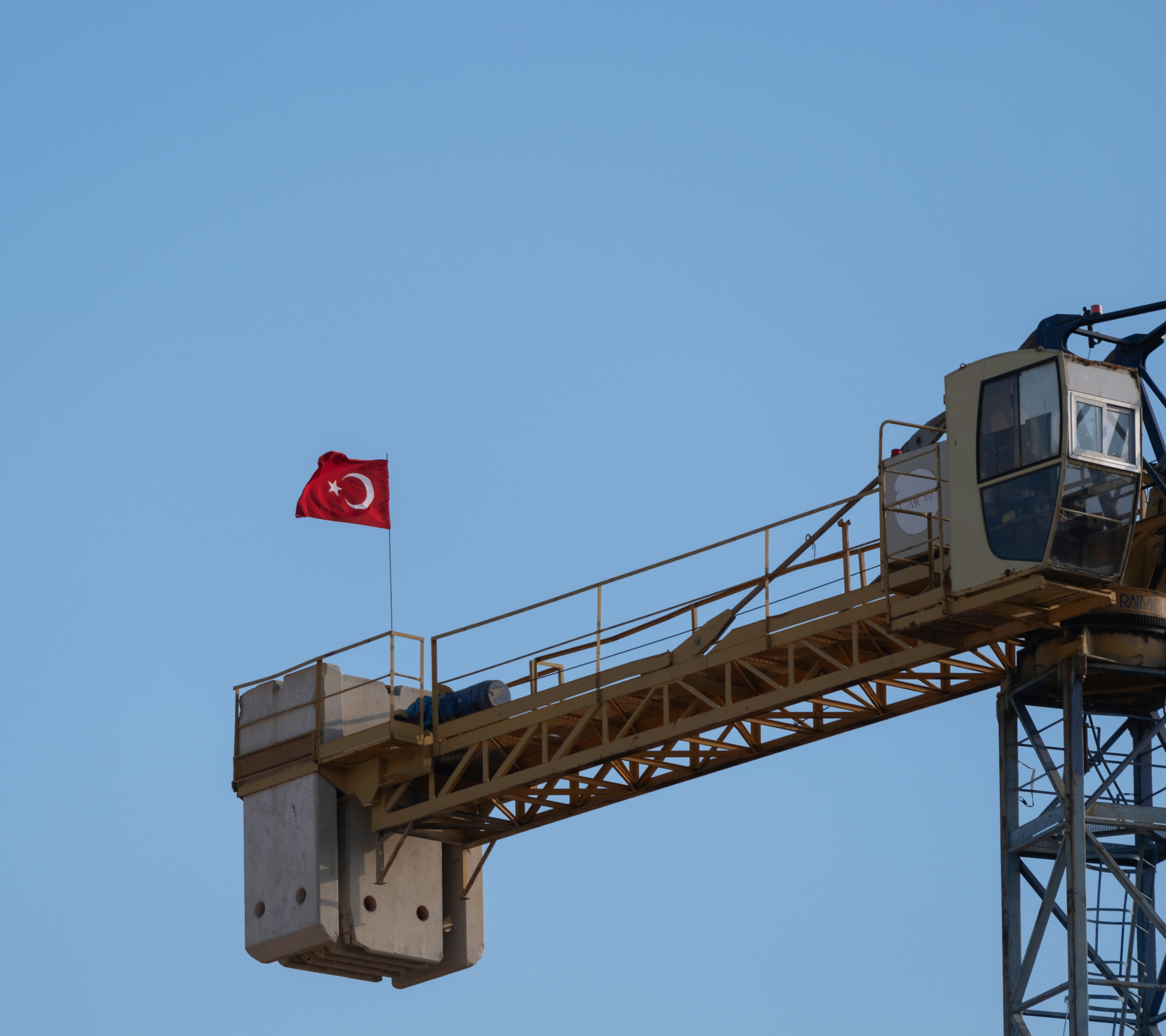 The flag of Turkey flying from a yellow construction crane against a blue sky